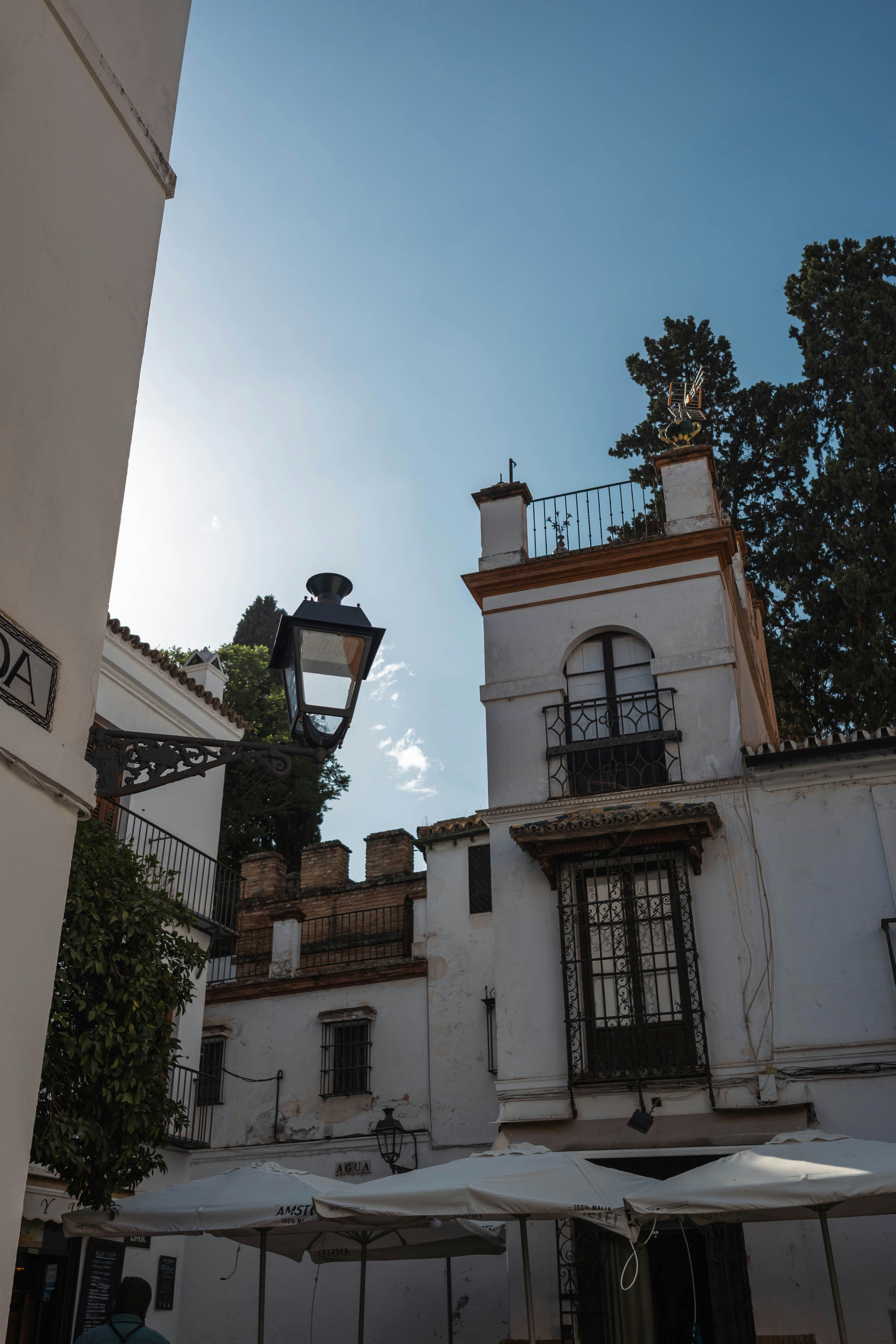Quiet Courtyard of White Facades: Lantern, Arches, and Café Umbrellas Under a Clear Sky