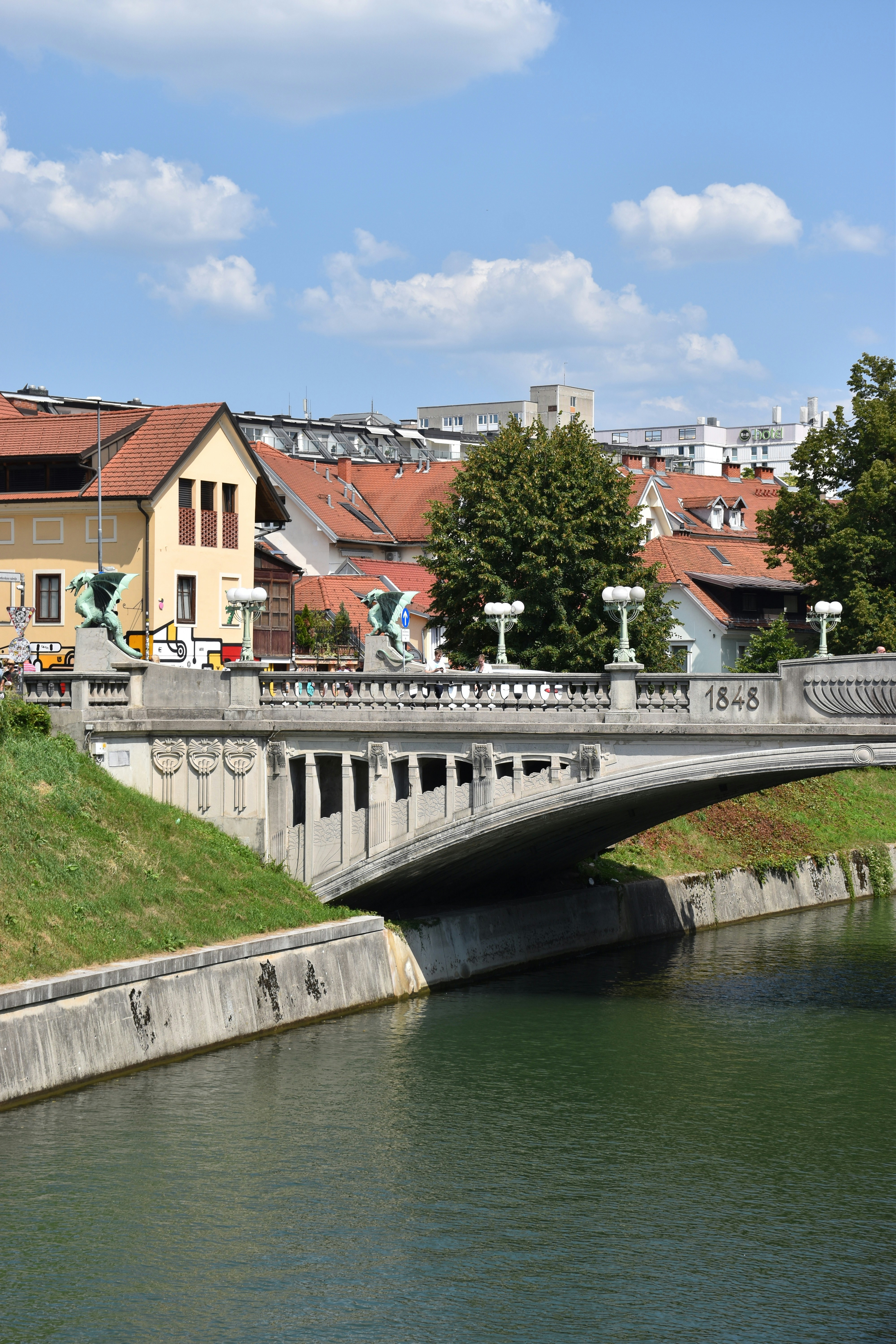 Historic bridge adorned with sculptures, spanning a tranquil river, flanked by colorful buildings under a clear blue sky.