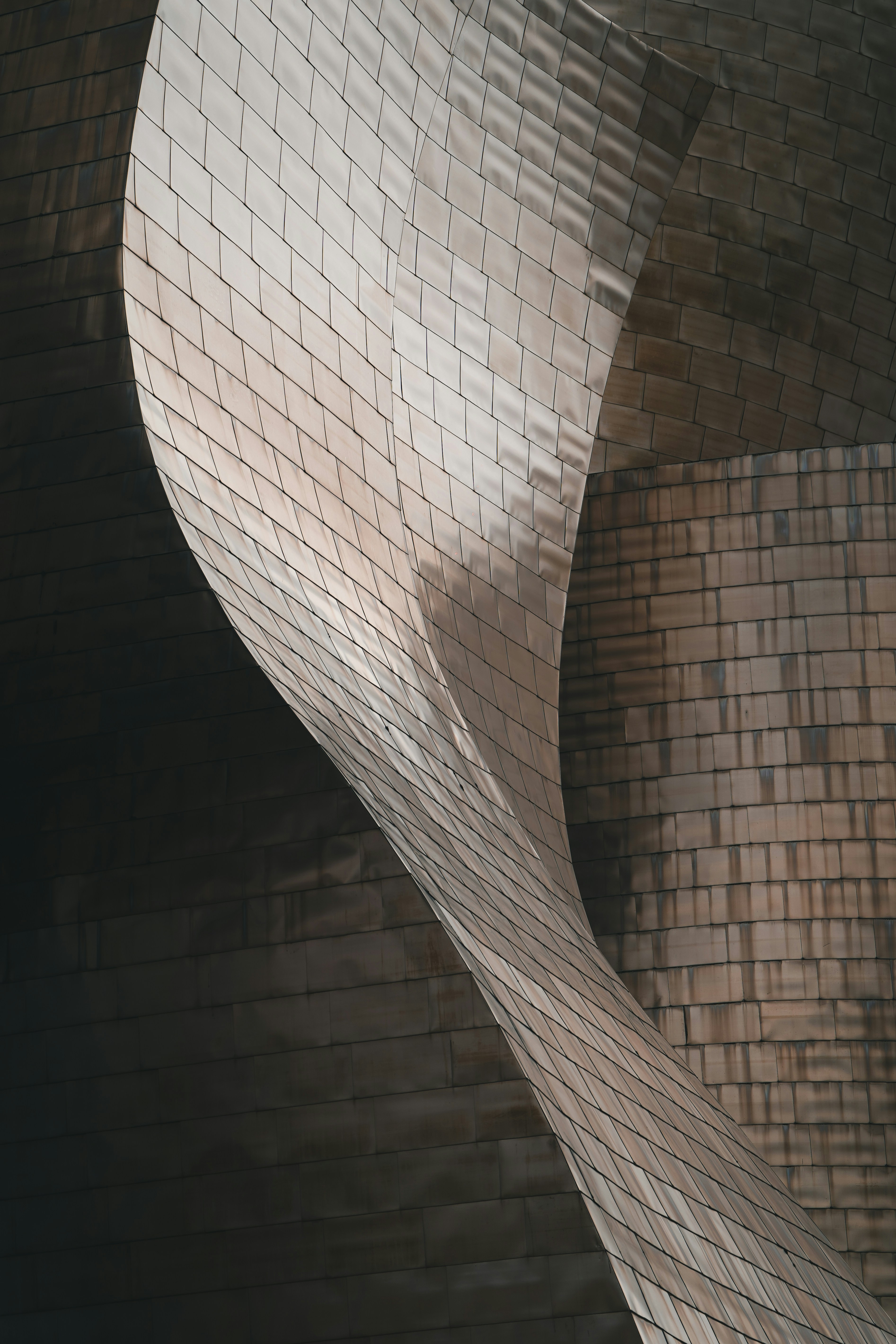 Curving metallic structure with tiled facade and shadowed sections.