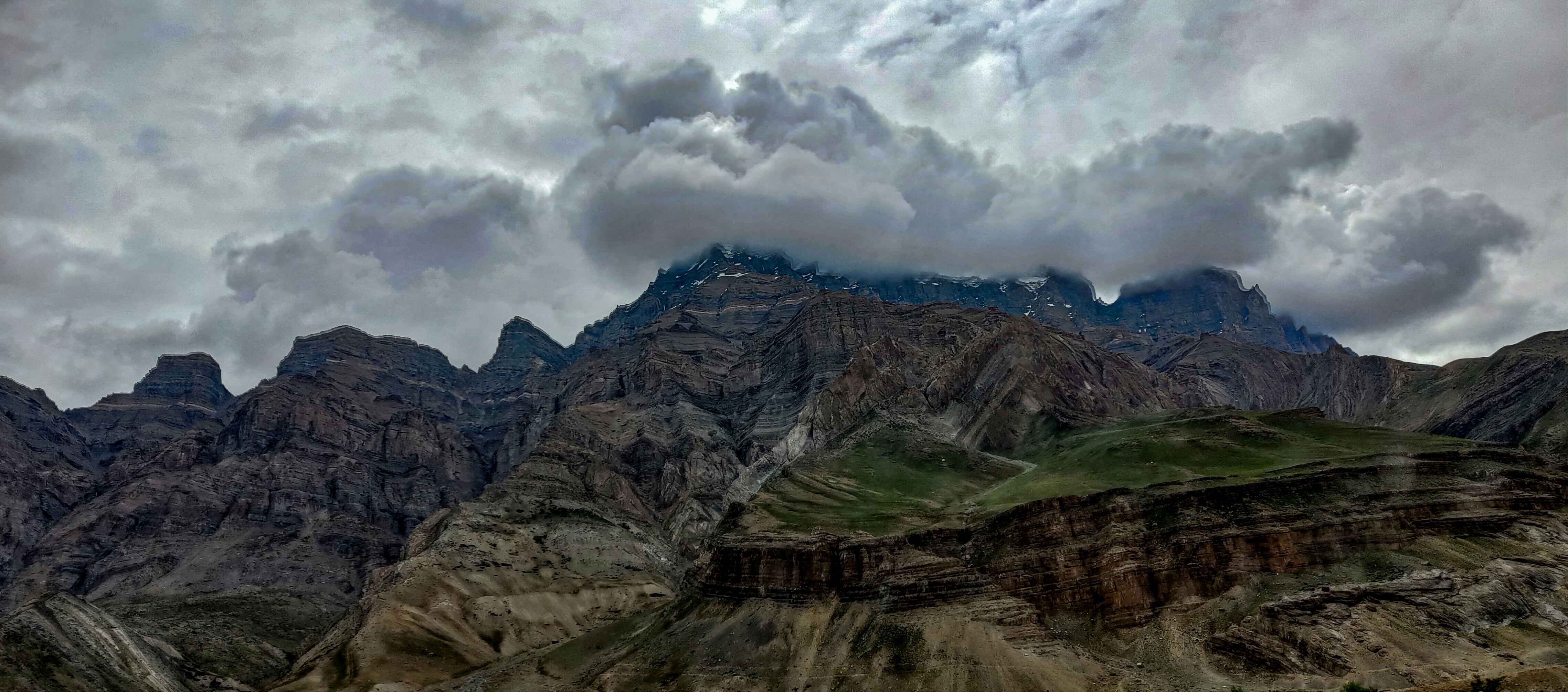 Dramatic mountain landscape shrouded in clouds, showcasing rugged terrain and sweeping cliffs. The scene evokes a sense of adventure and mystery.