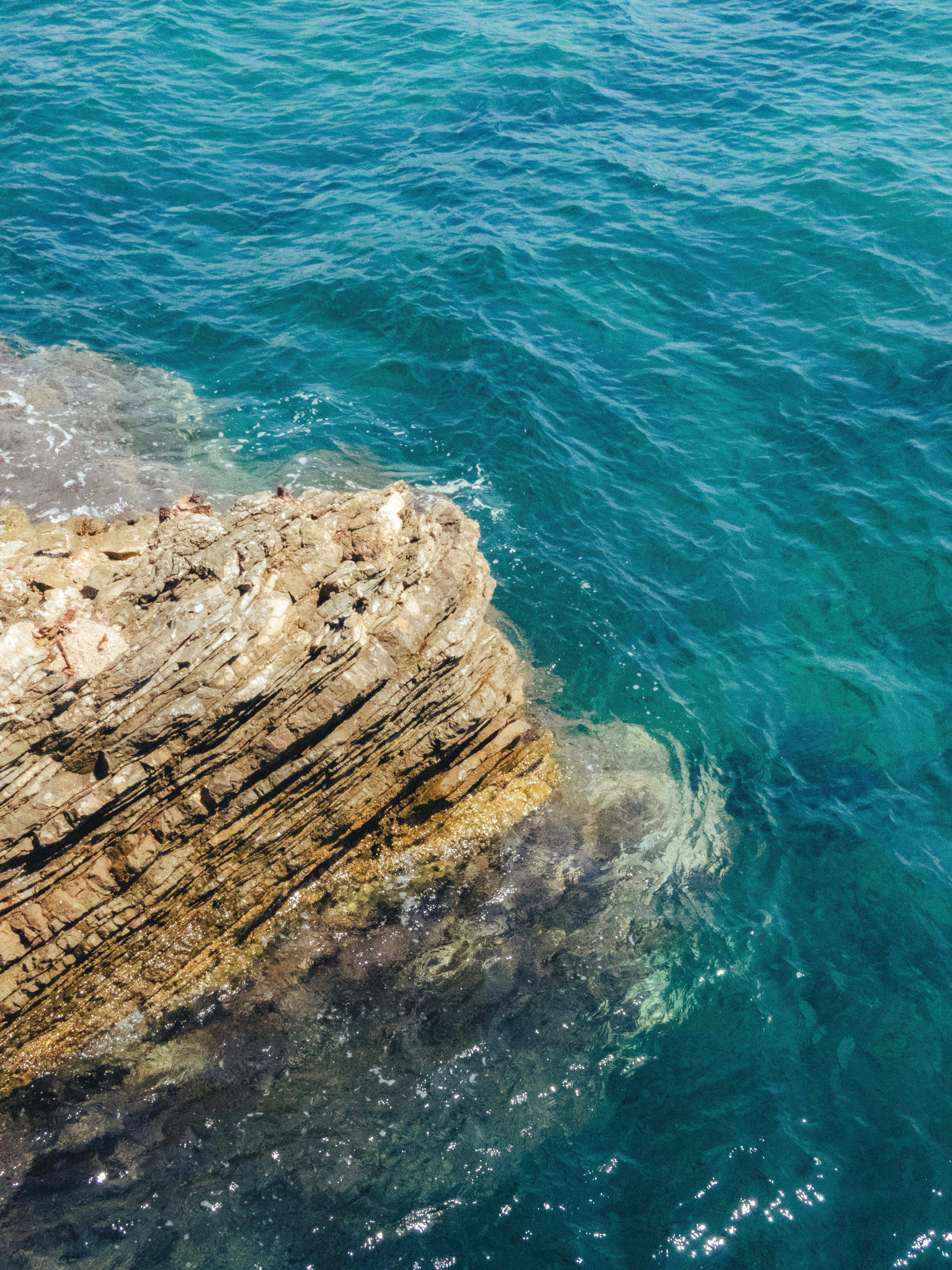 Sunlit rock formation meeting the vibrant turquoise waters of the Adriatic Sea | Rocky shore meets clear turquoise ocean water