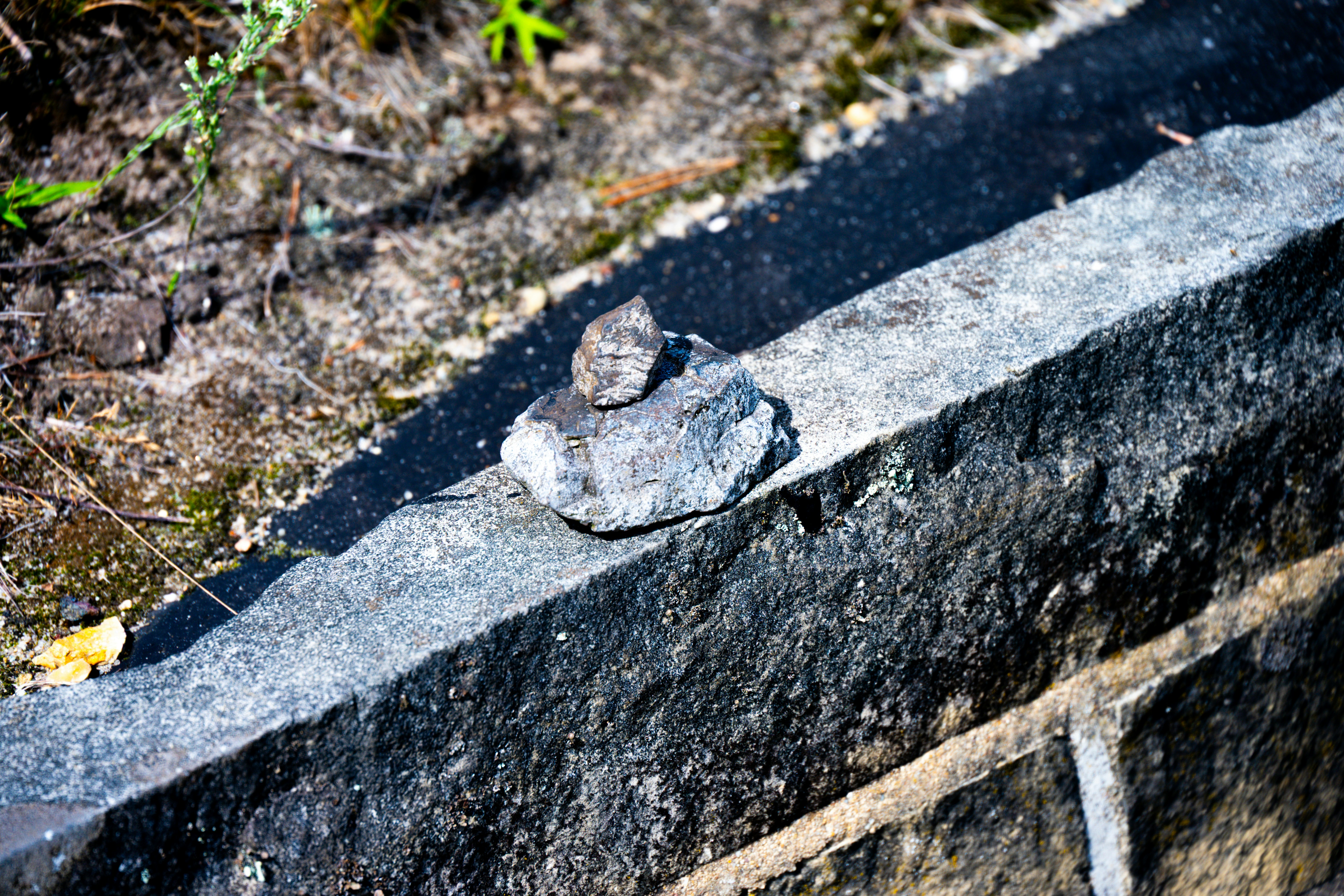 Two stones balanced atop a rough stone surface, surrounded by natural elements. The scene captures a moment of harmony in the outdoors.