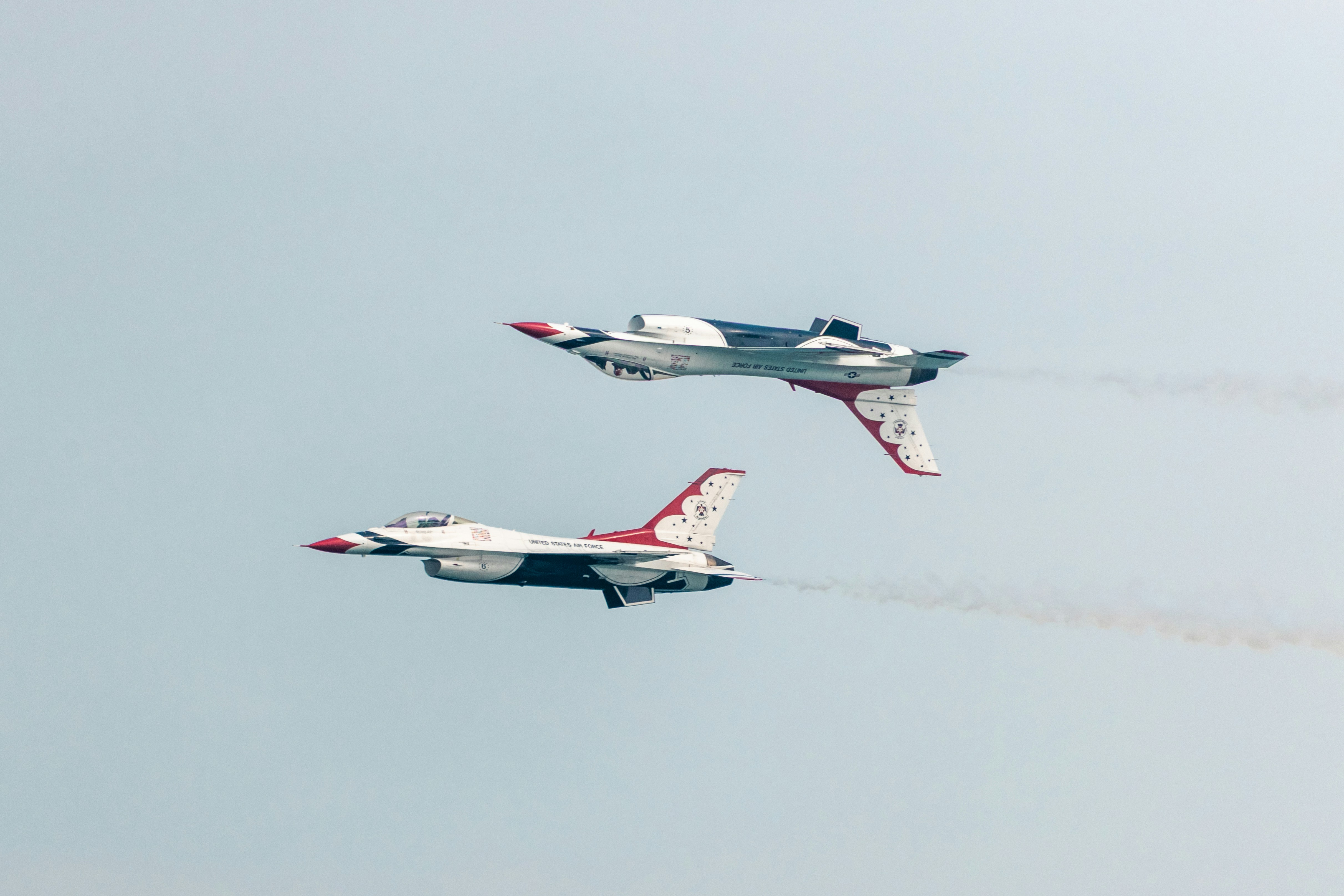 Two fighter jets perform a synchronized maneuver against a clear sky, showcasing their aerodynamic design and agility.