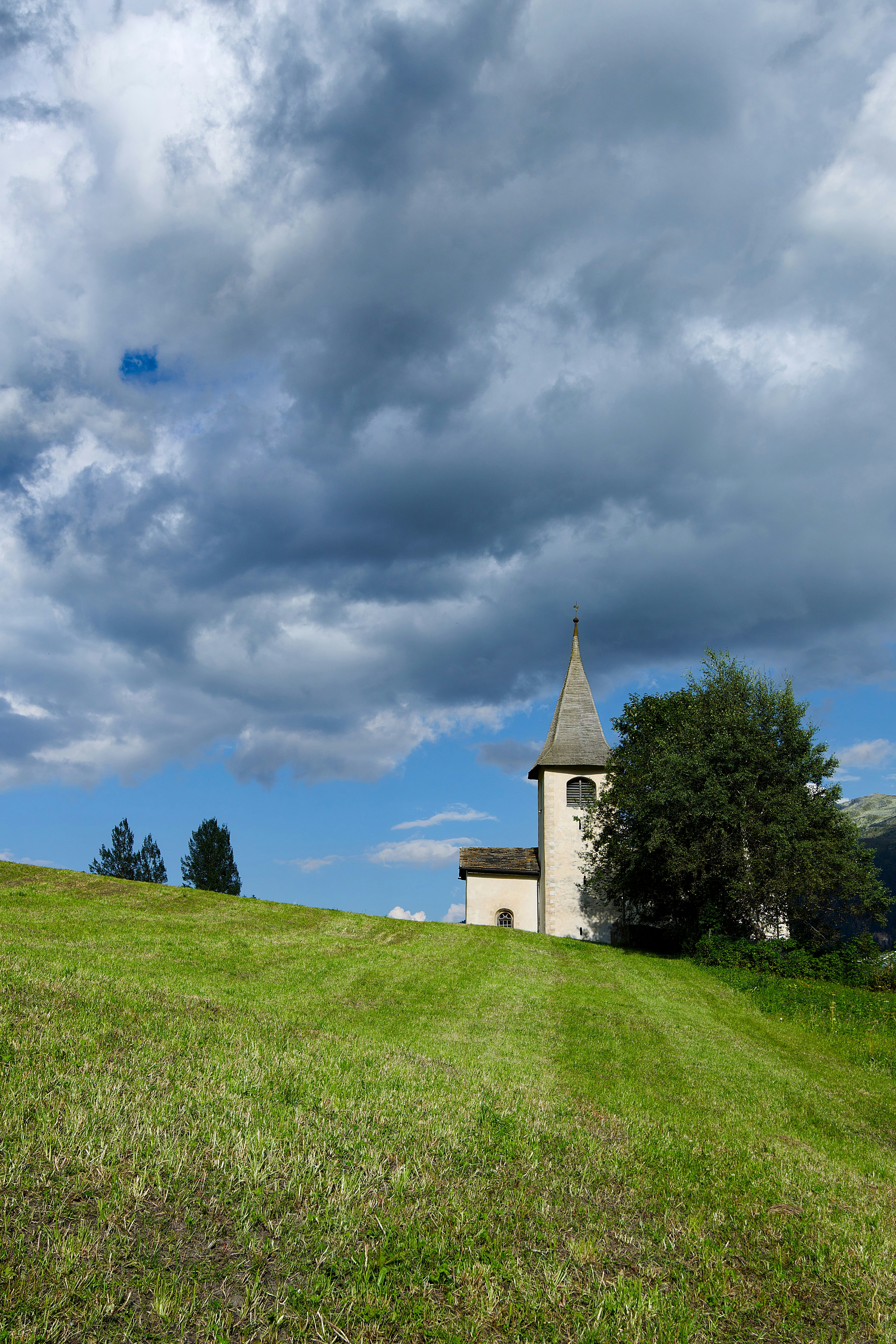 Reformierte Kirche Medels | A church on a grassy hill under stormy clouds
