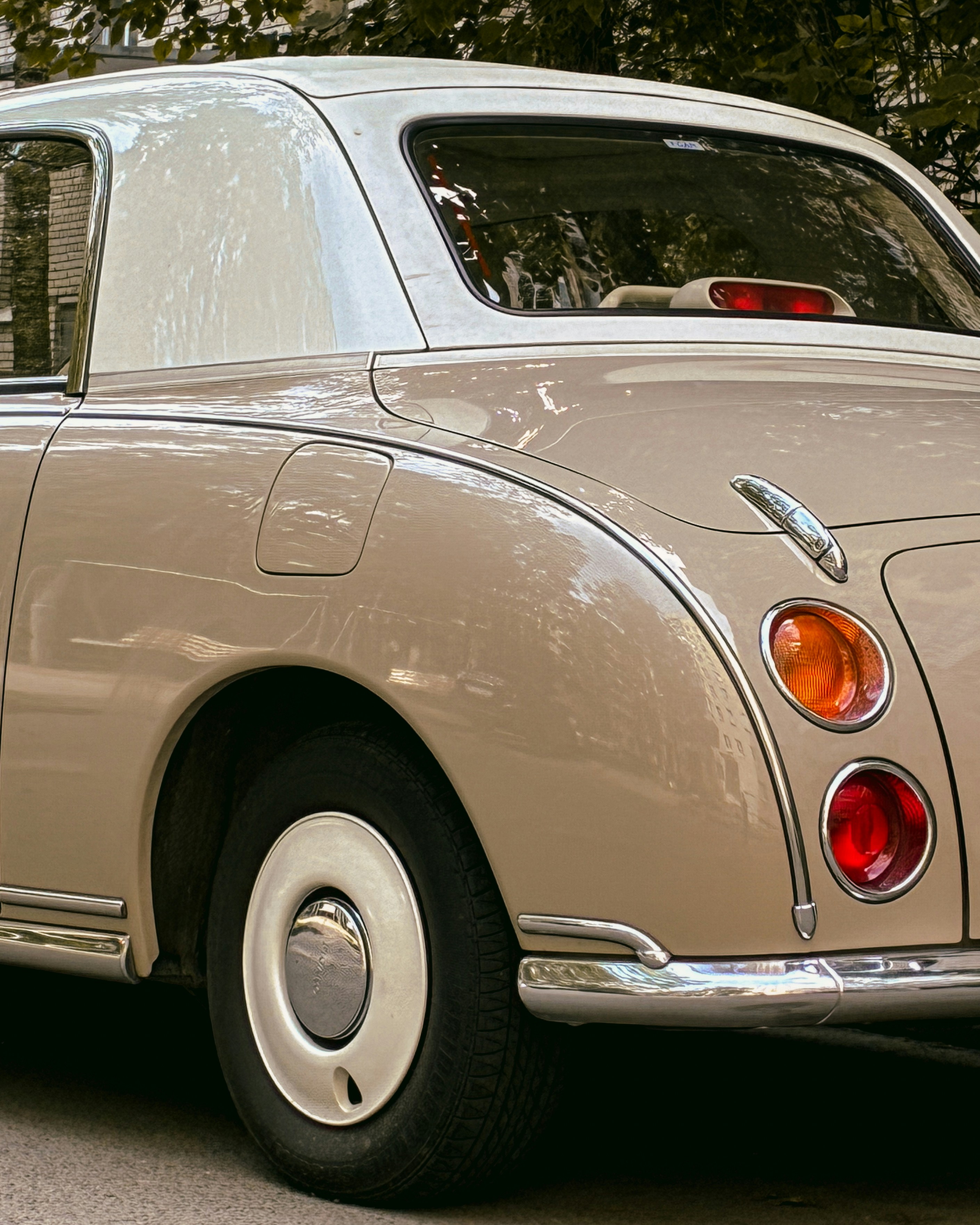 Classic car with a two-tone paint job parked under leafy trees, showcasing vintage design elements and smooth curves.