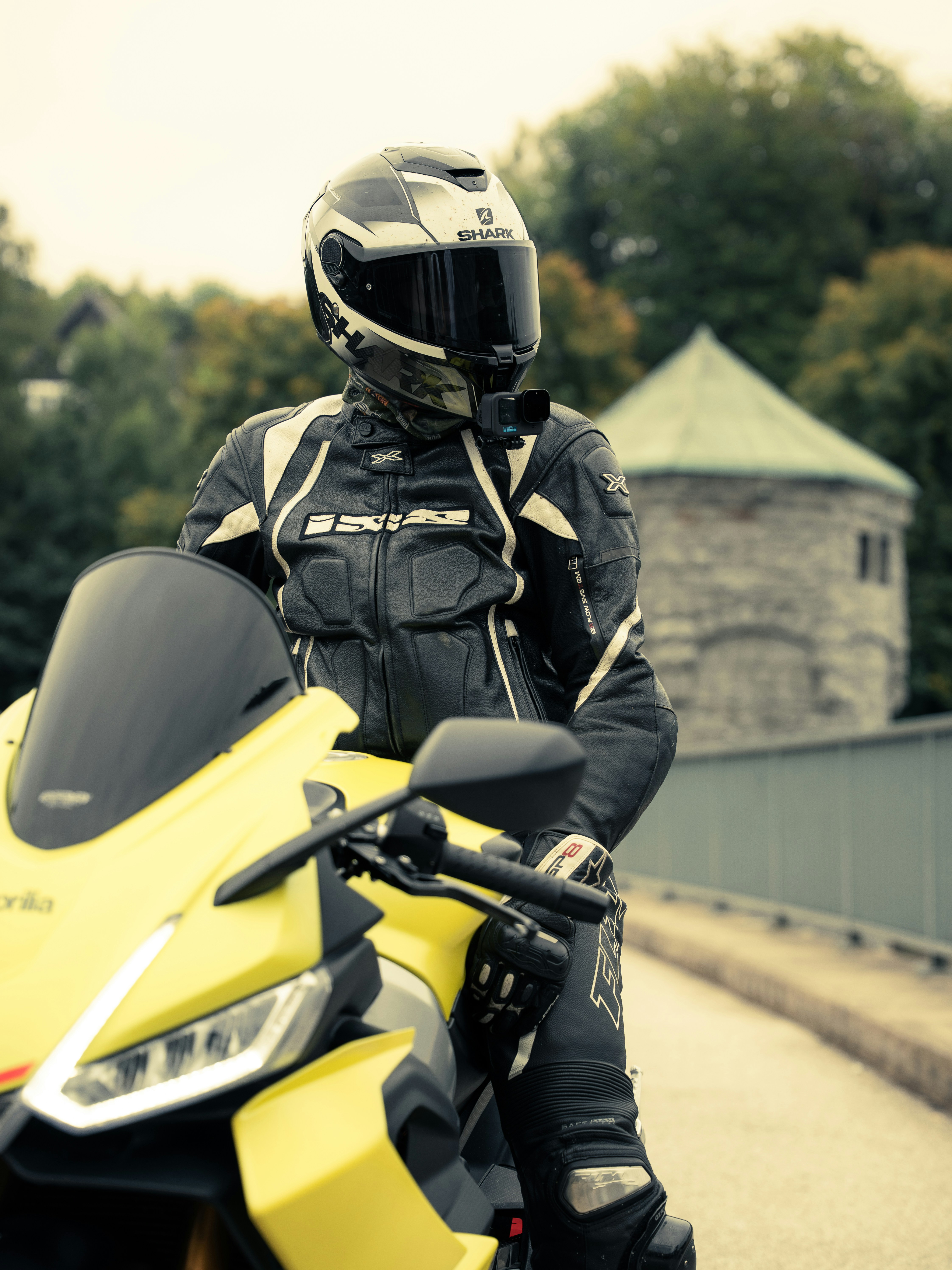 Motorcyclist in sleek black and yellow gear poised on a vibrant motorcycle, with a stone structure in the background. 