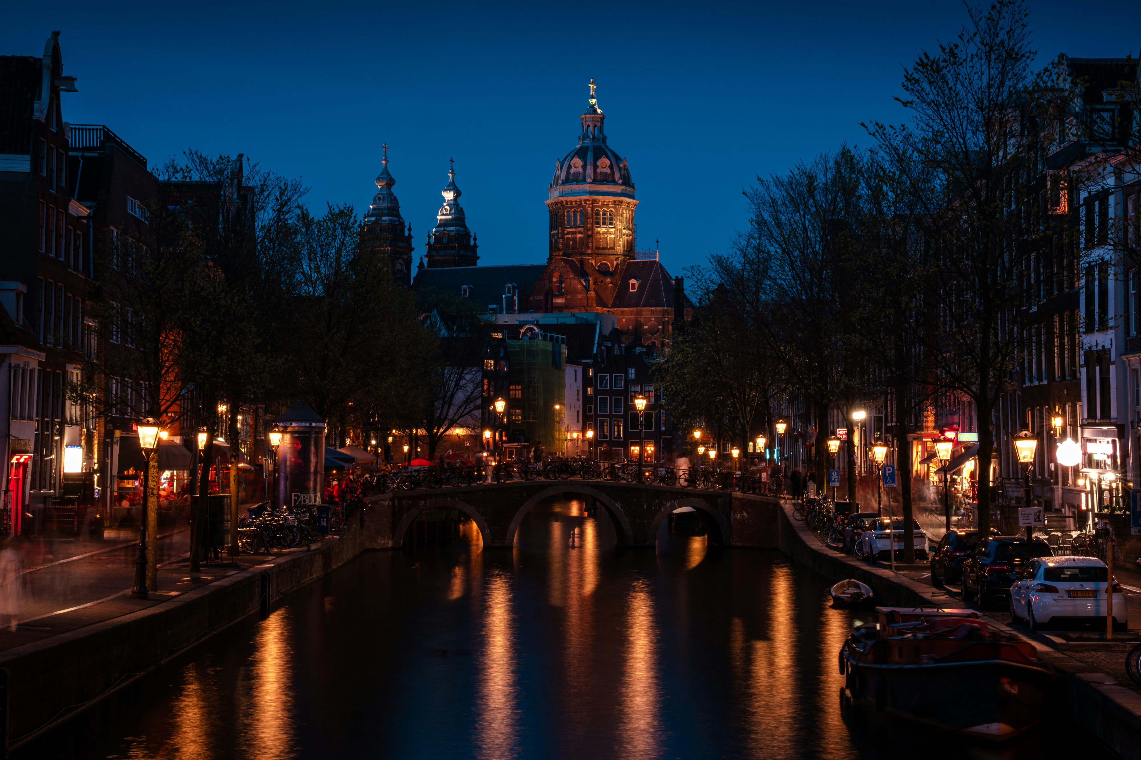Historic buildings lining a serene canal illuminated by streetlights at twilight, showcasing the charm of Amsterdam's architecture and waterways.