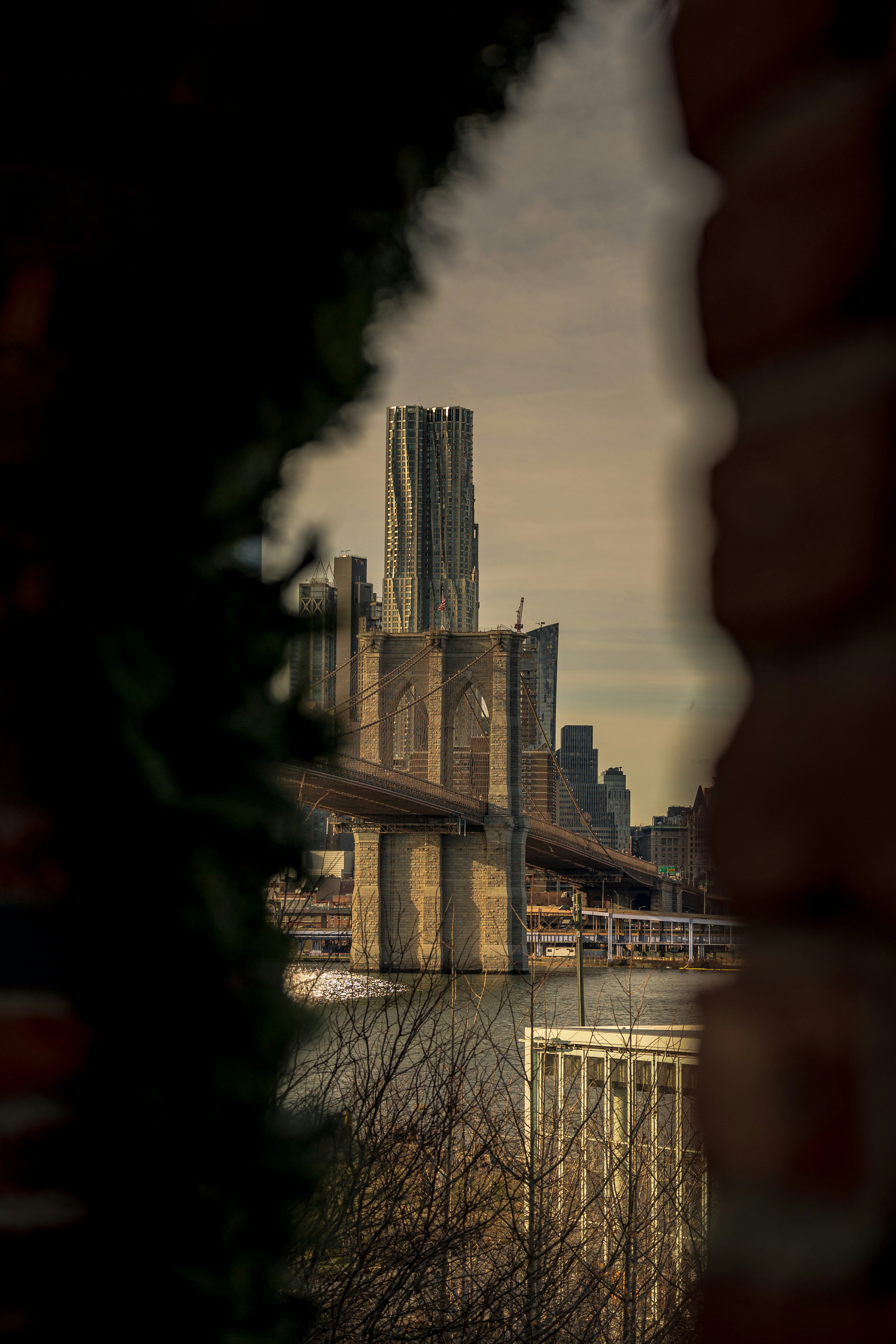Brooklyn Bridge framed by a natural arch, showcasing the contrast between historic architecture and modern skyscrapers. 
