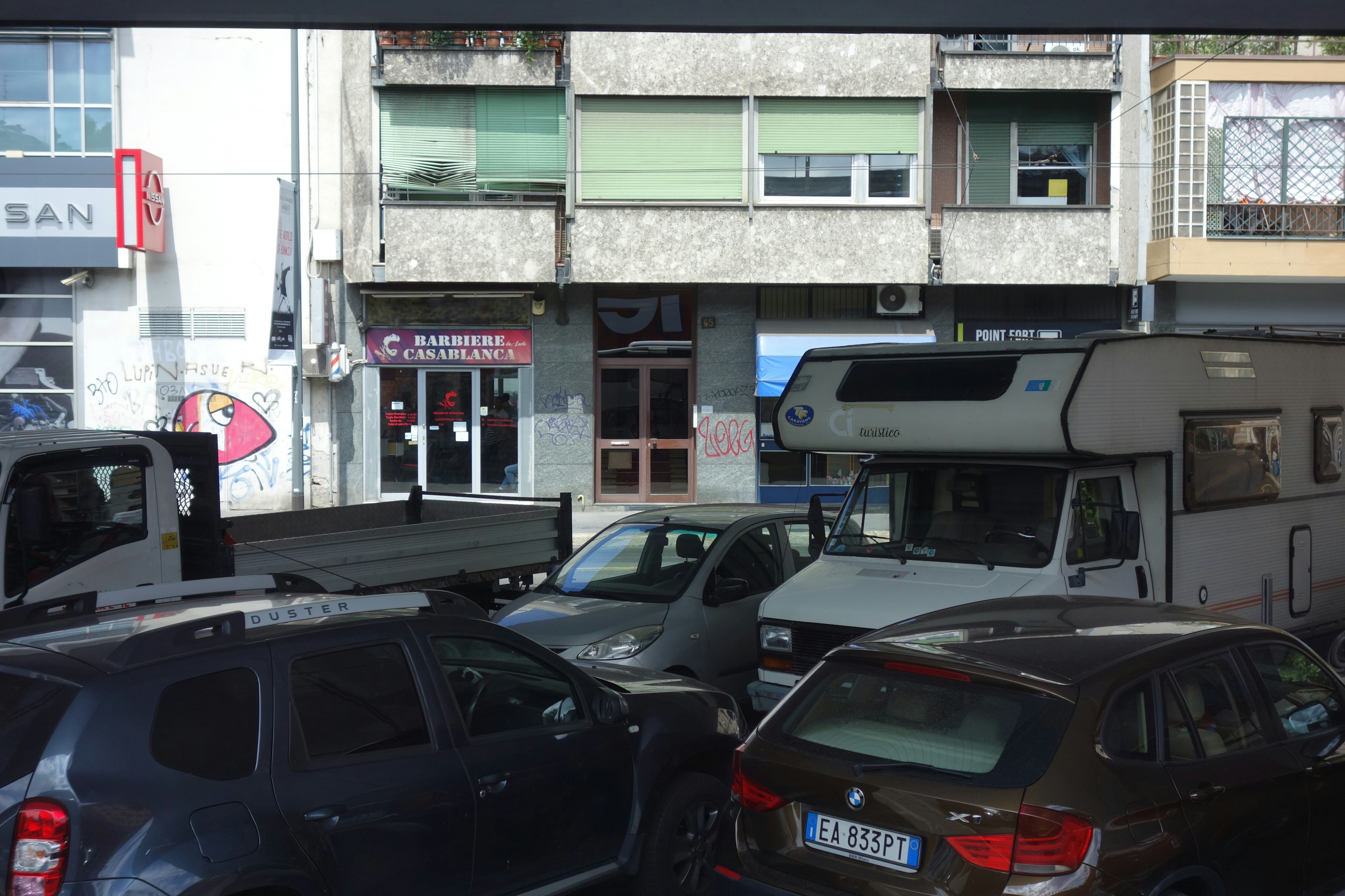 A crowded street scene featuring various vehicles obstructing the view of a building with a distinct sign. The setting encapsulates the hustle and bustle of urban environments.