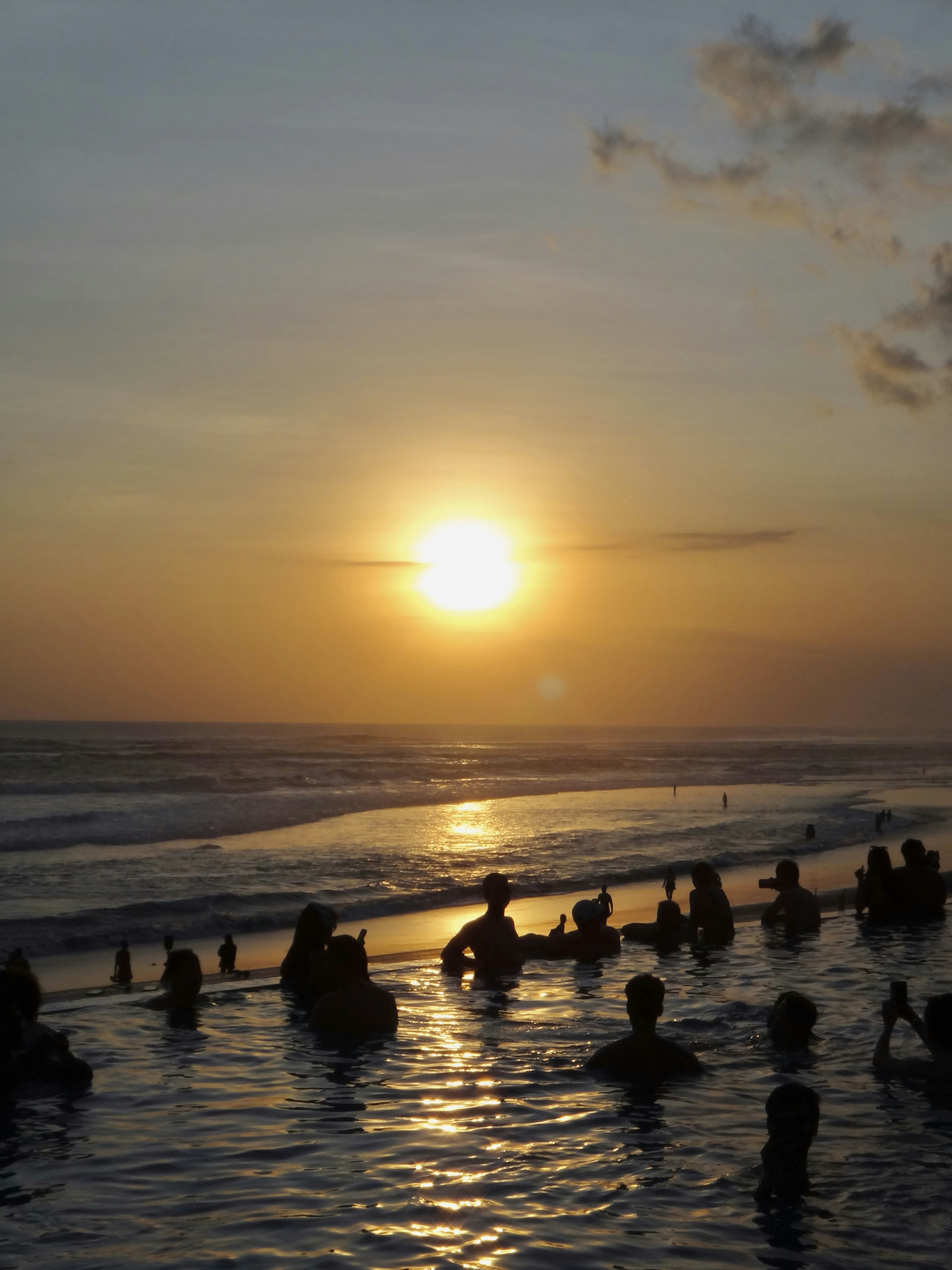 Ocean beach view from the poolside | People swimming in infinity pool at sunset