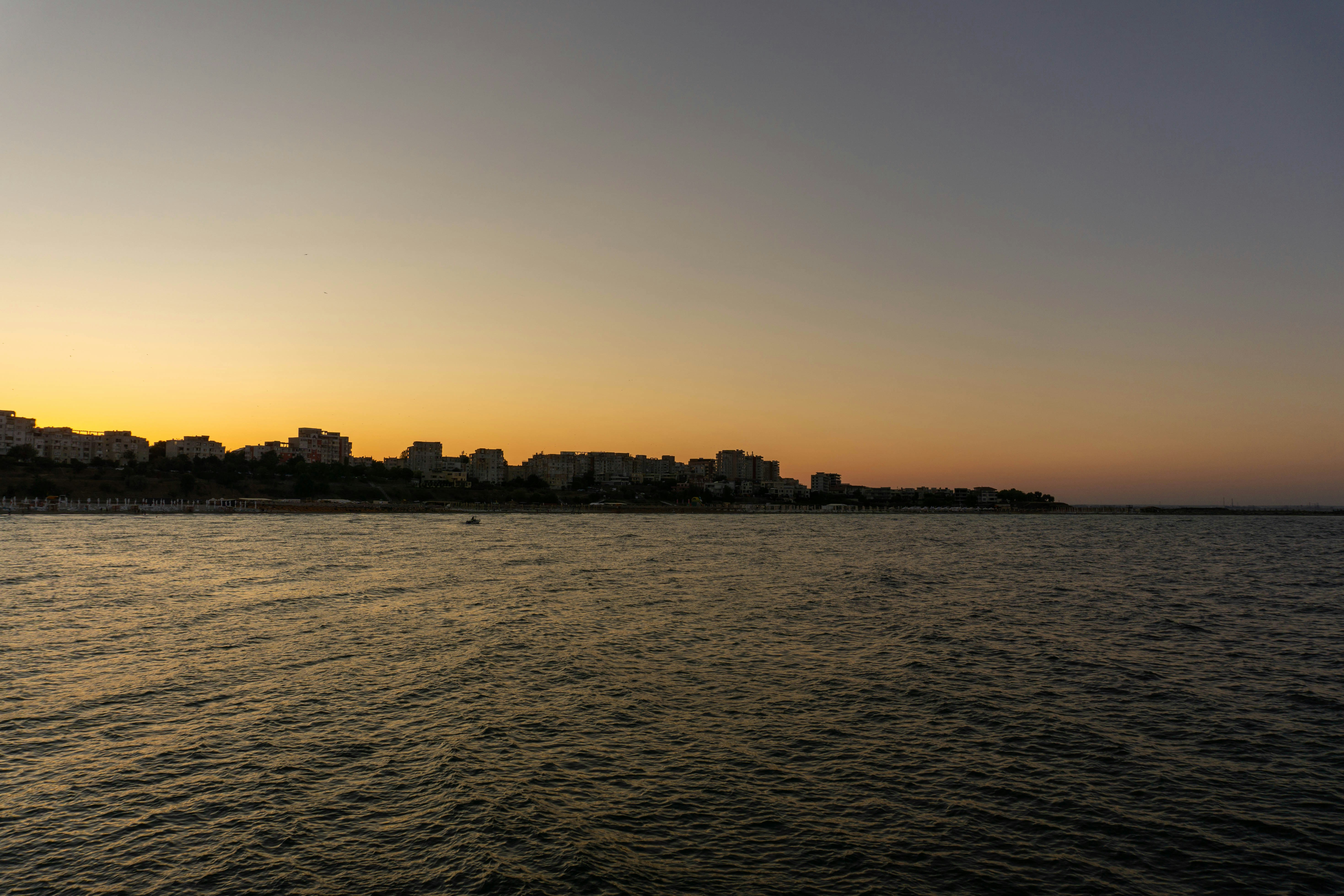 Sunset over the calm ocean with a distant city skyline.