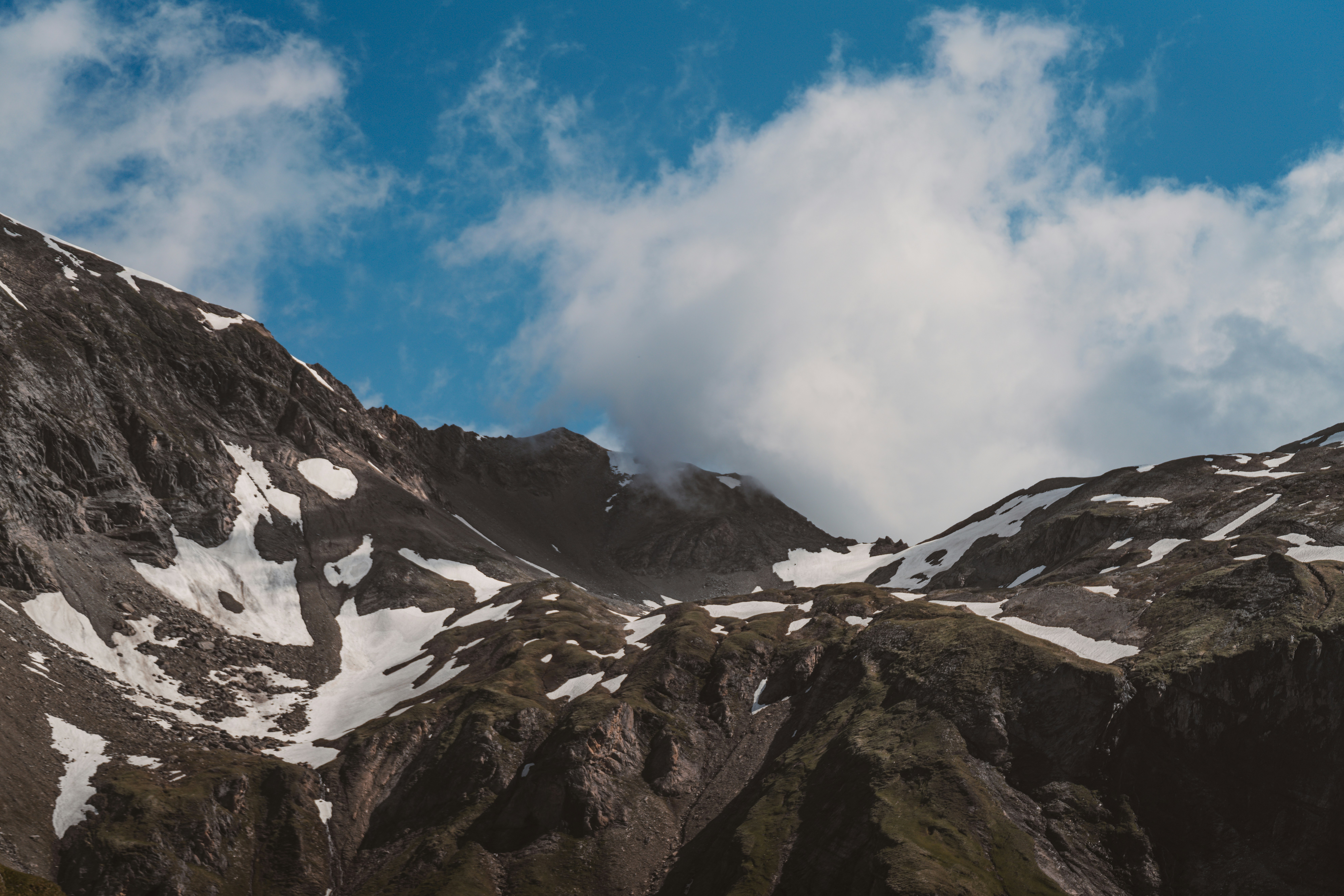 Snowy mountain ridge under blue sky | Snow-capped mountains under a blue sky with clouds