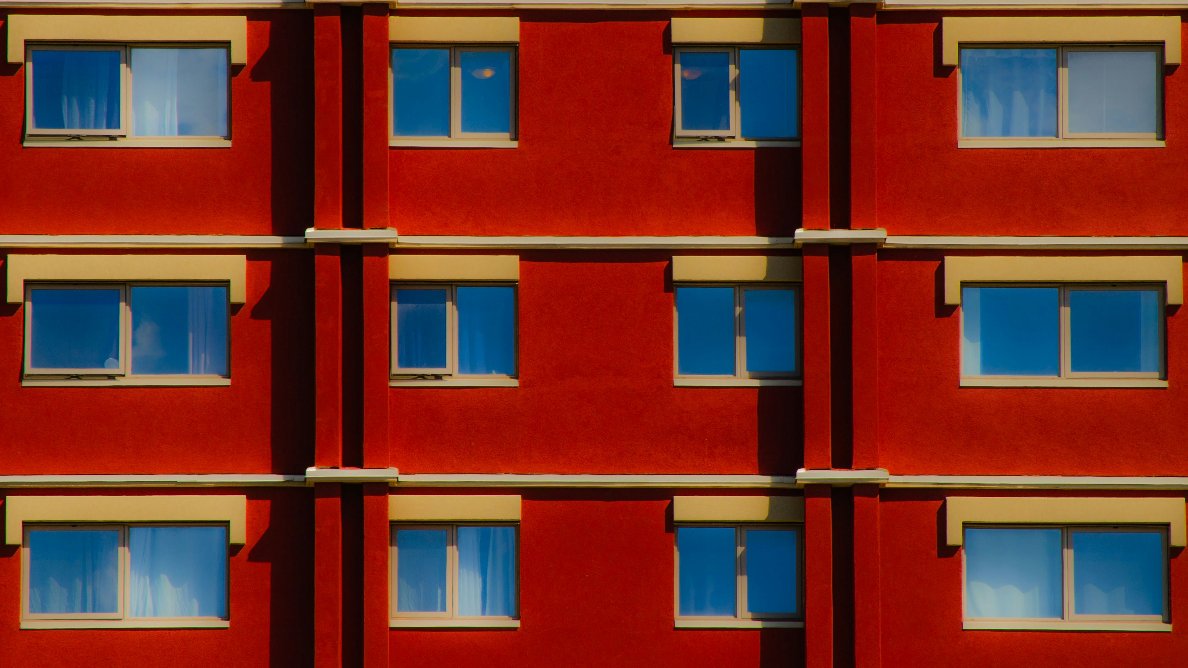 A brightly coloured modern building facade emphasizing geometric patterns and vibrant hues. | Red building facade with multiple windows
