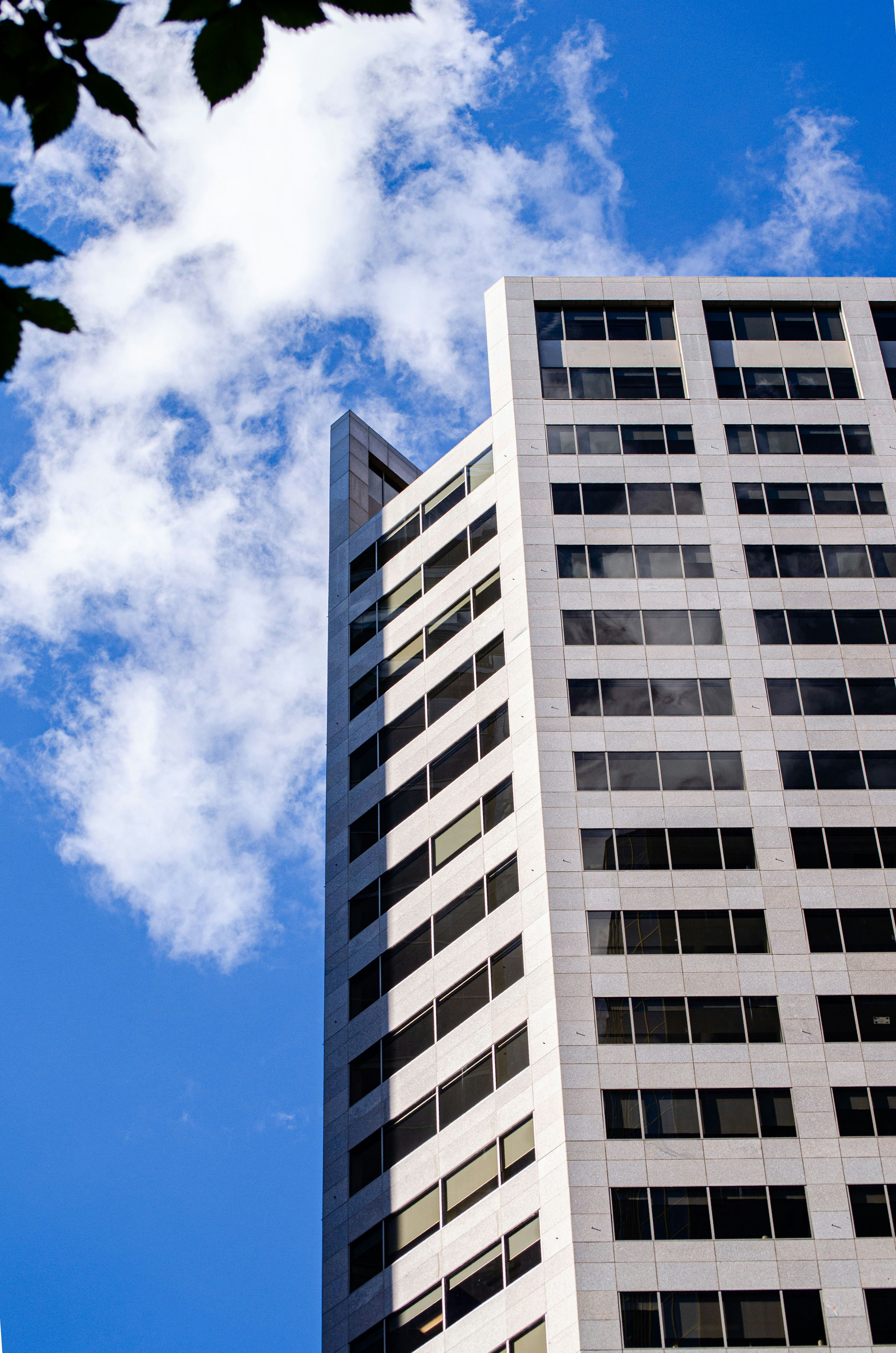 A tall office building reaches for the sky against a backdrop of blue and white clouds, showcasing contemporary design elements.