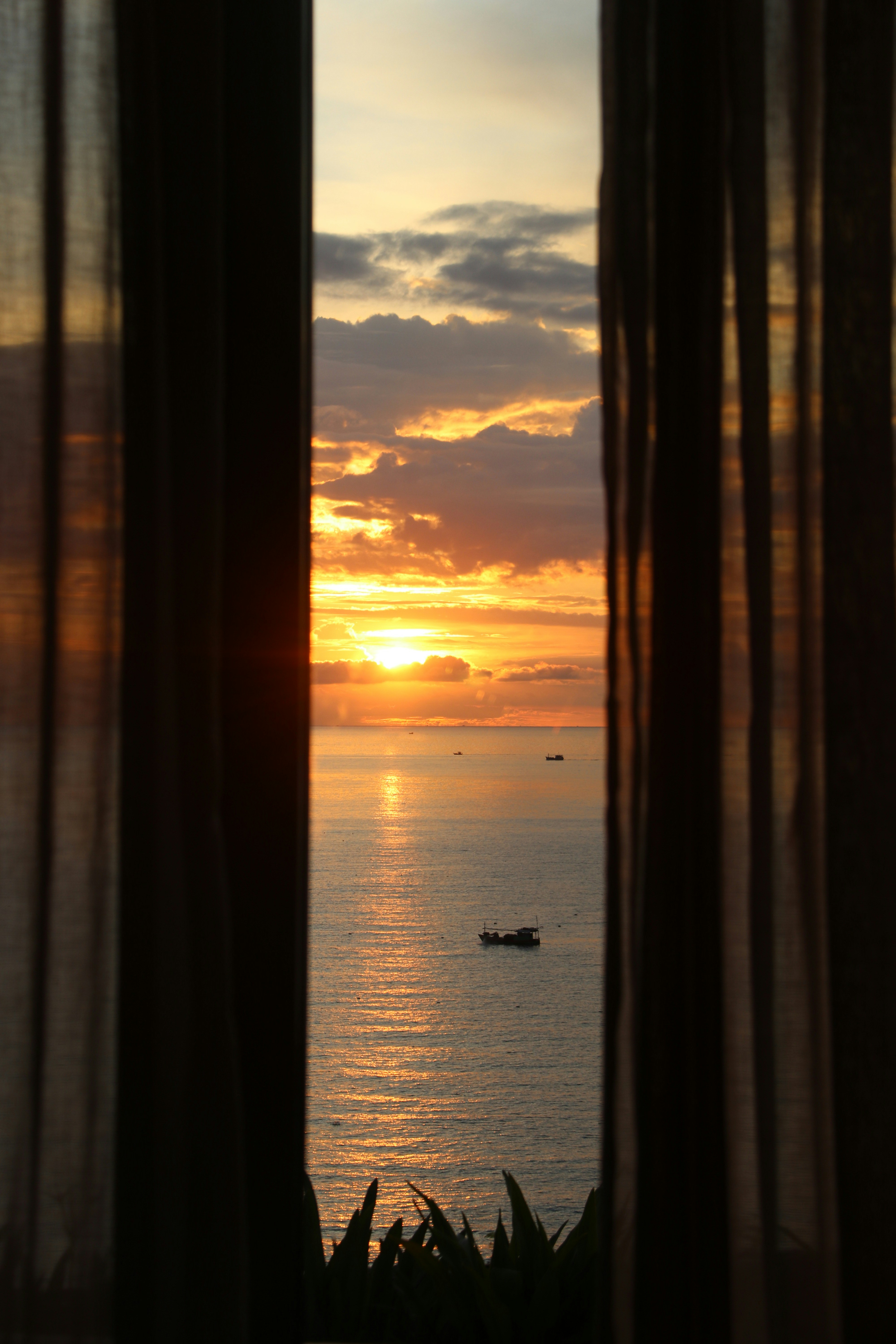 Curtains of Twilight: Sunset Framed Between Veiled Windows Over a Calm Sea