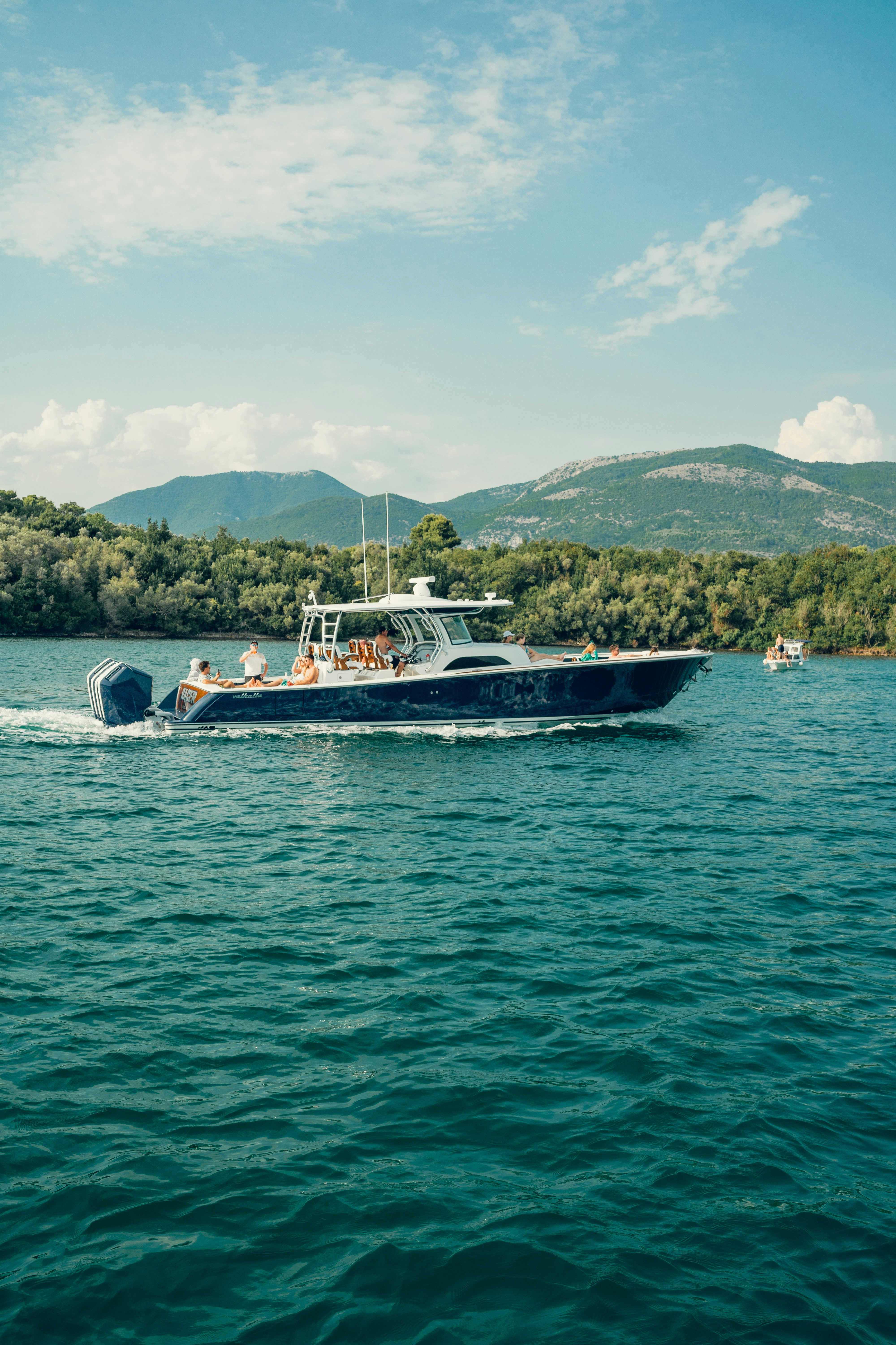 A motorboat cruises across a blue bay with green hills.