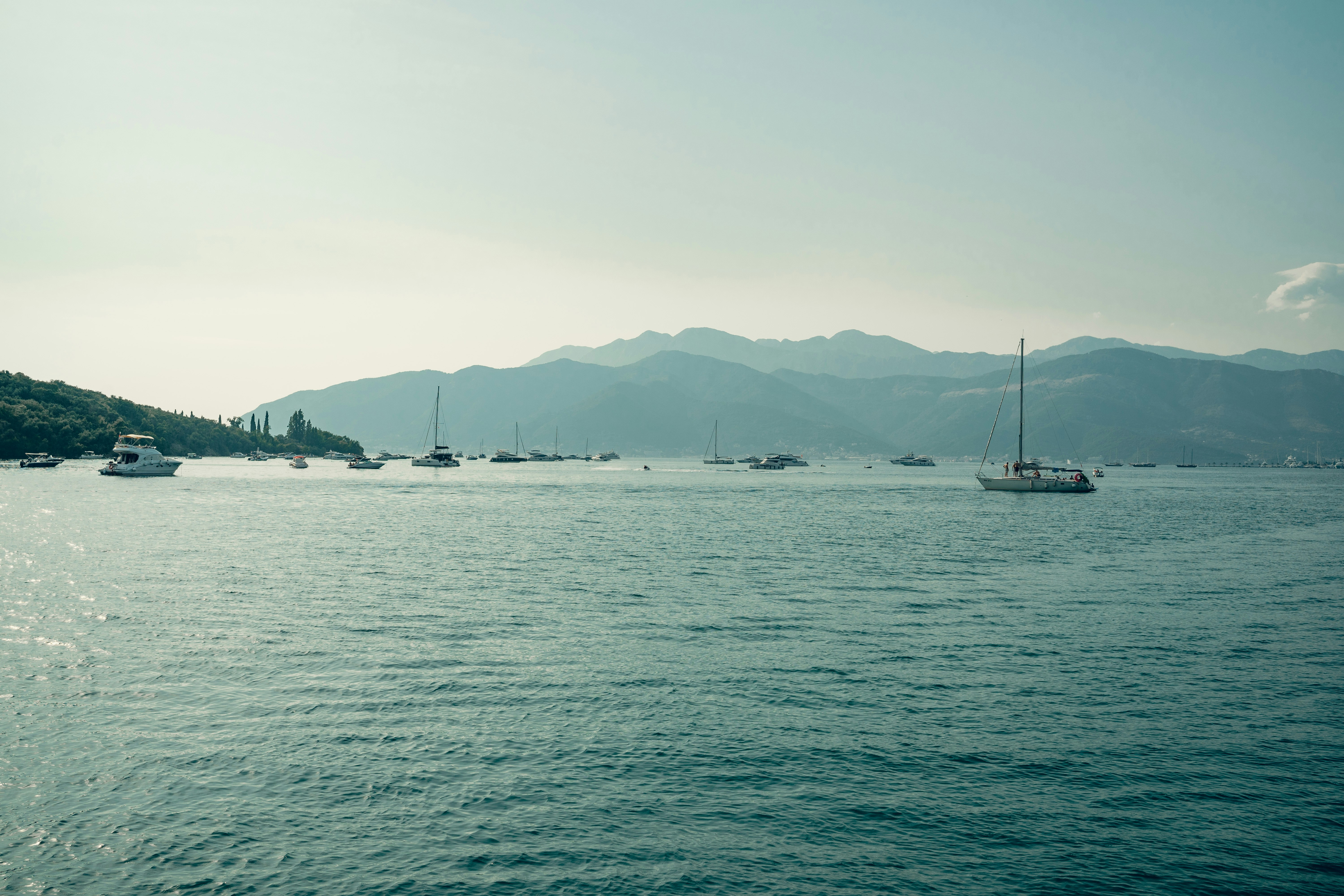 Sailboats and yachts anchored in a bay with mountains.