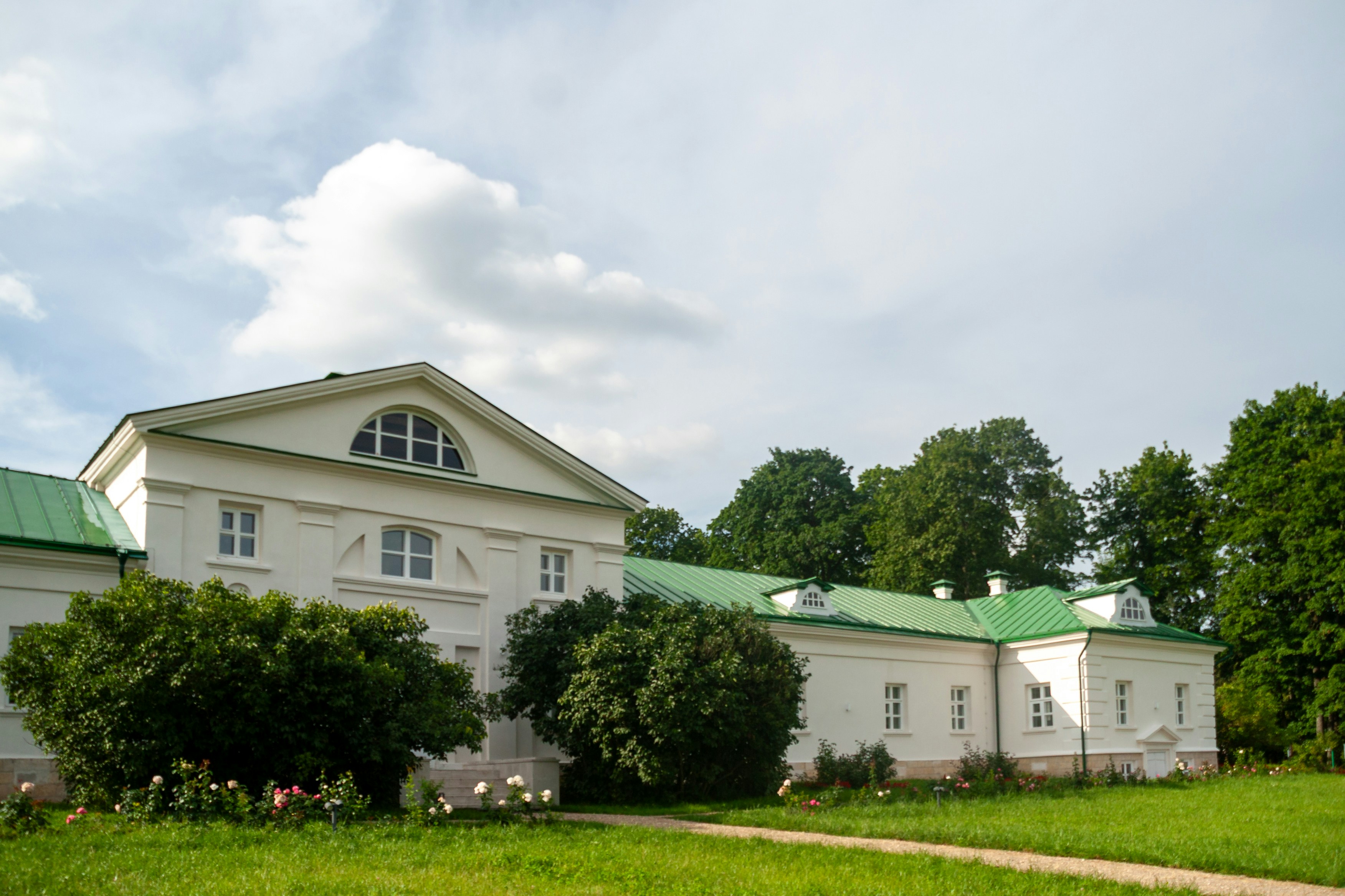 White manor house with green roof and trees.
