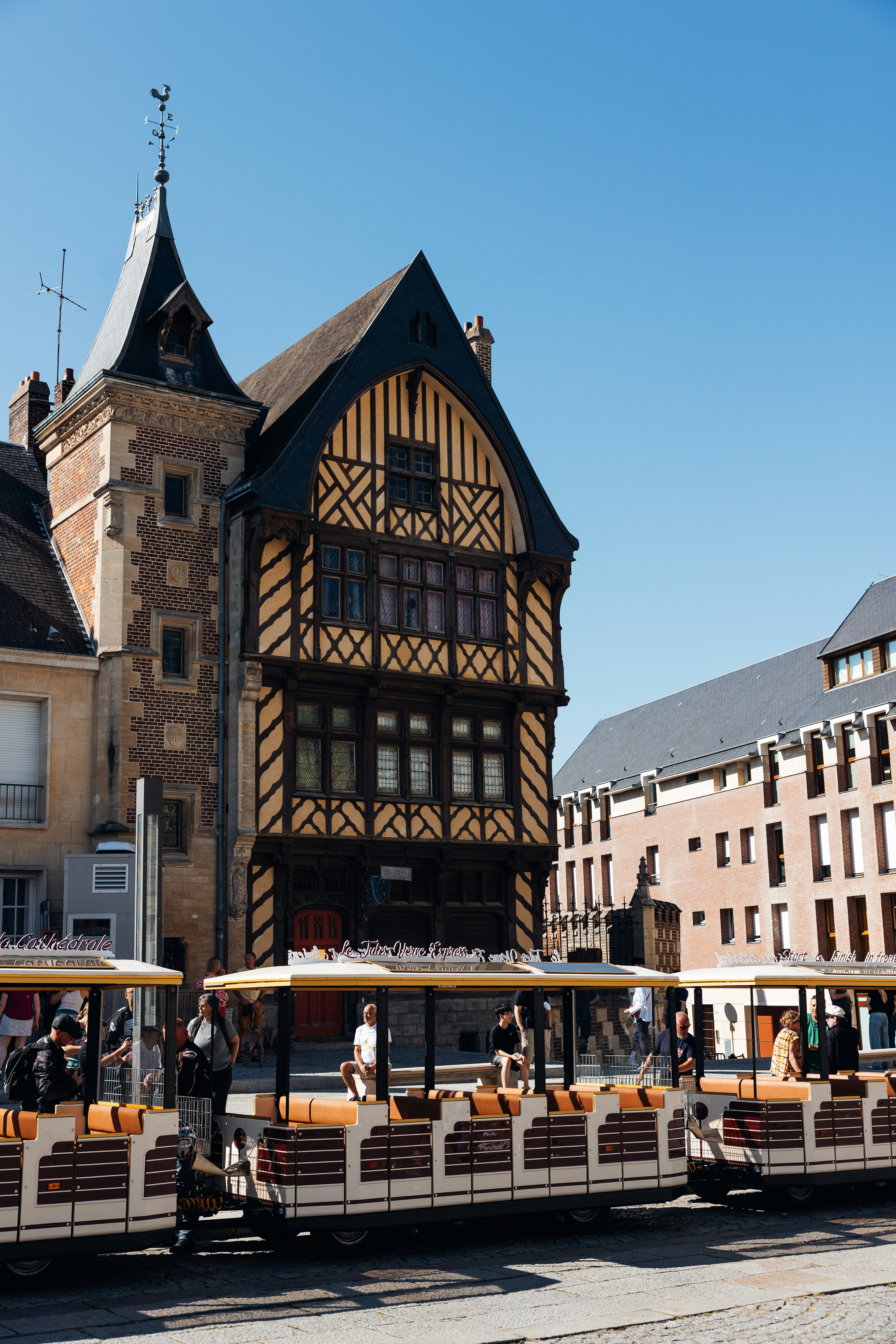 Charming half-timbered building stands proudly alongside a tourist train in a bustling town square.