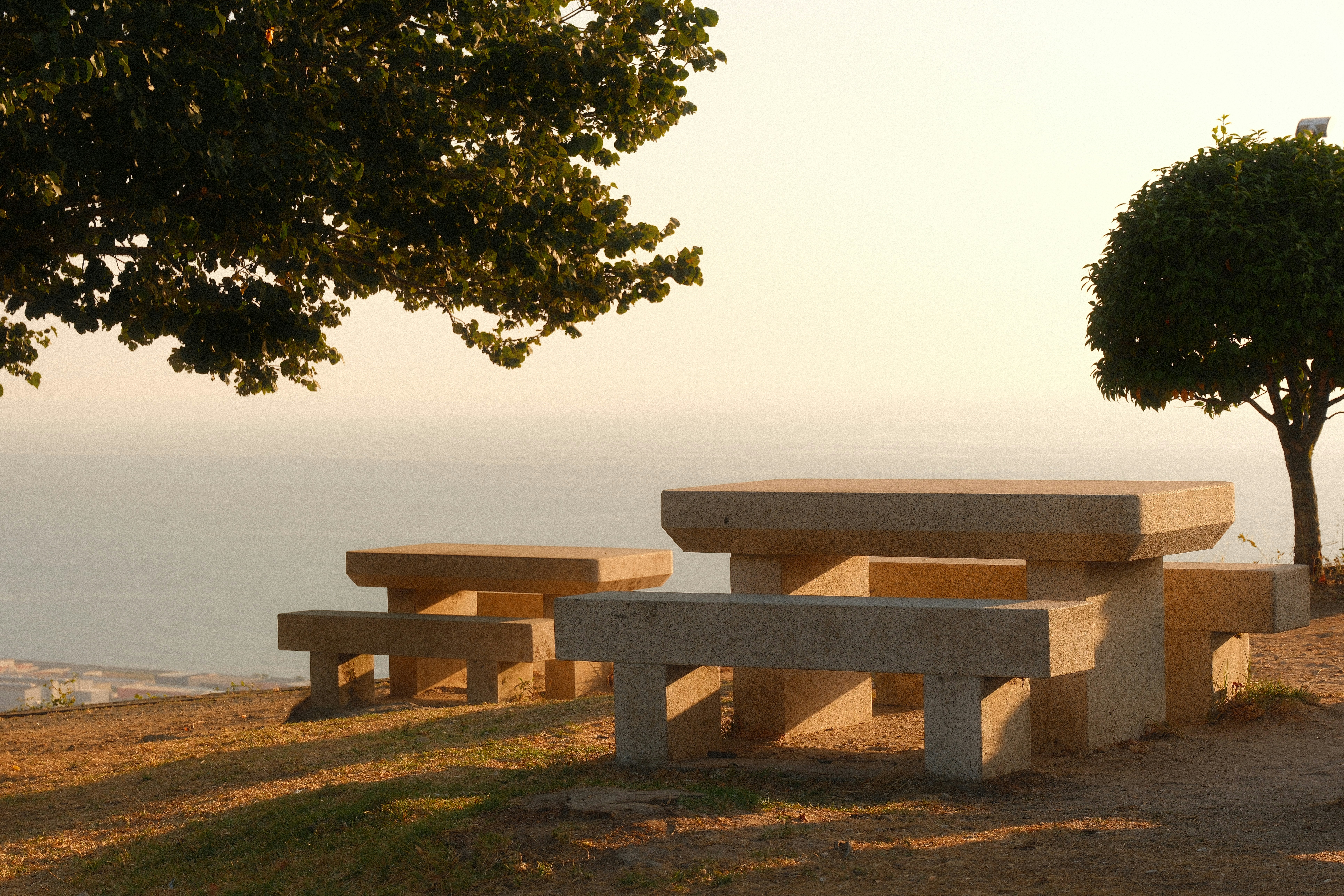 Stone picnic tables under trees overlooking the ocean.