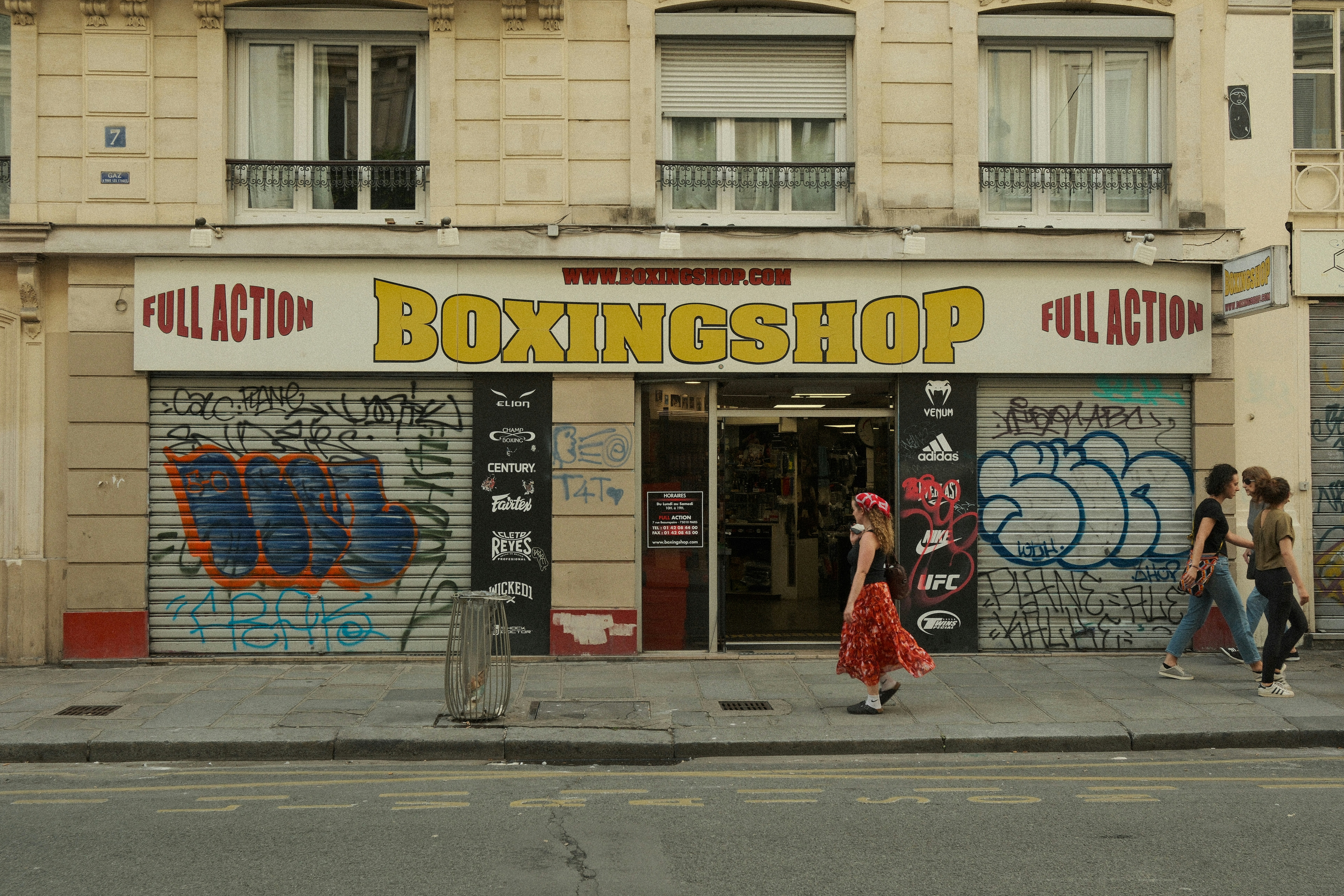 People walk past a boxing shop with graffiti