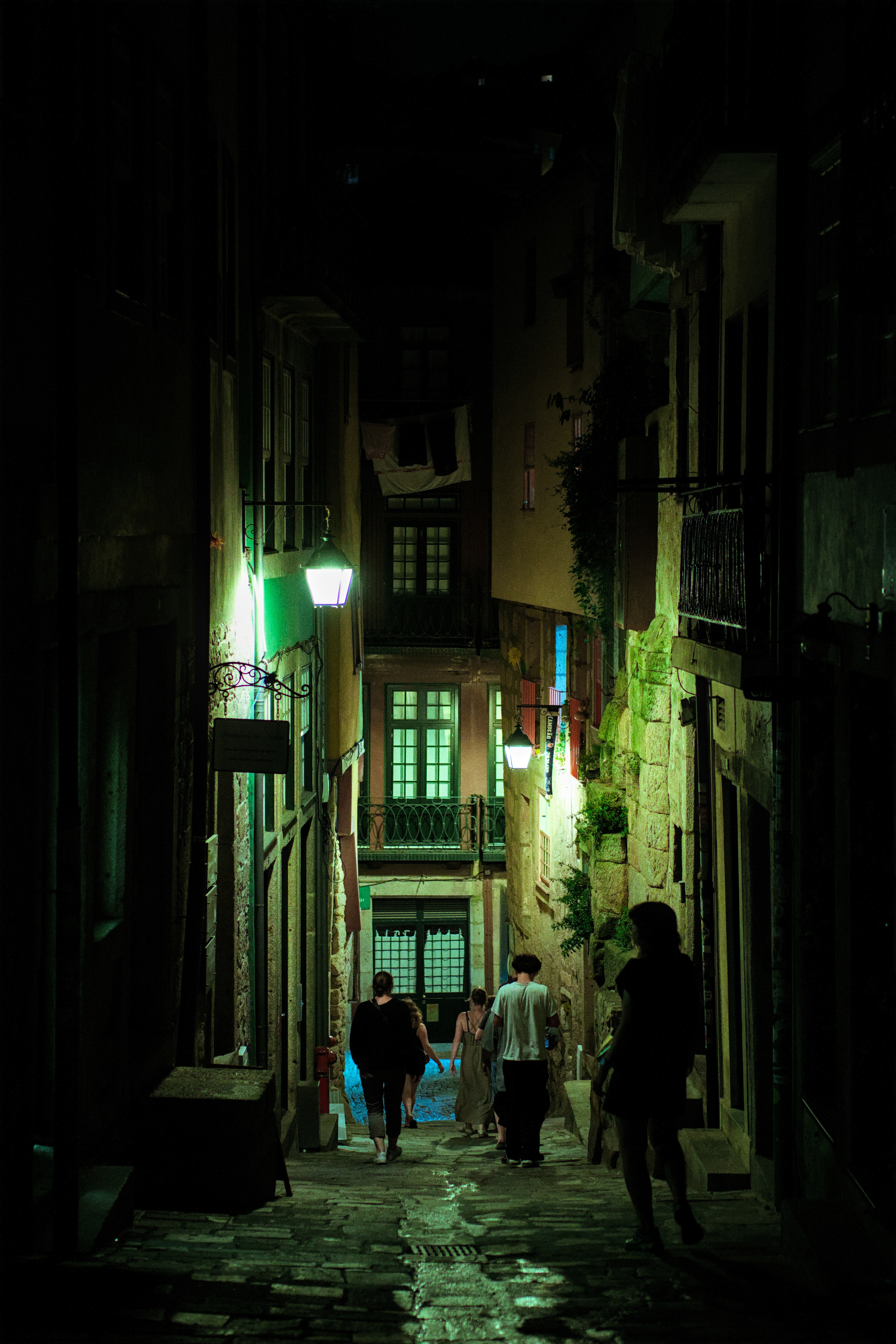 People walk down a narrow cobblestone street at night.