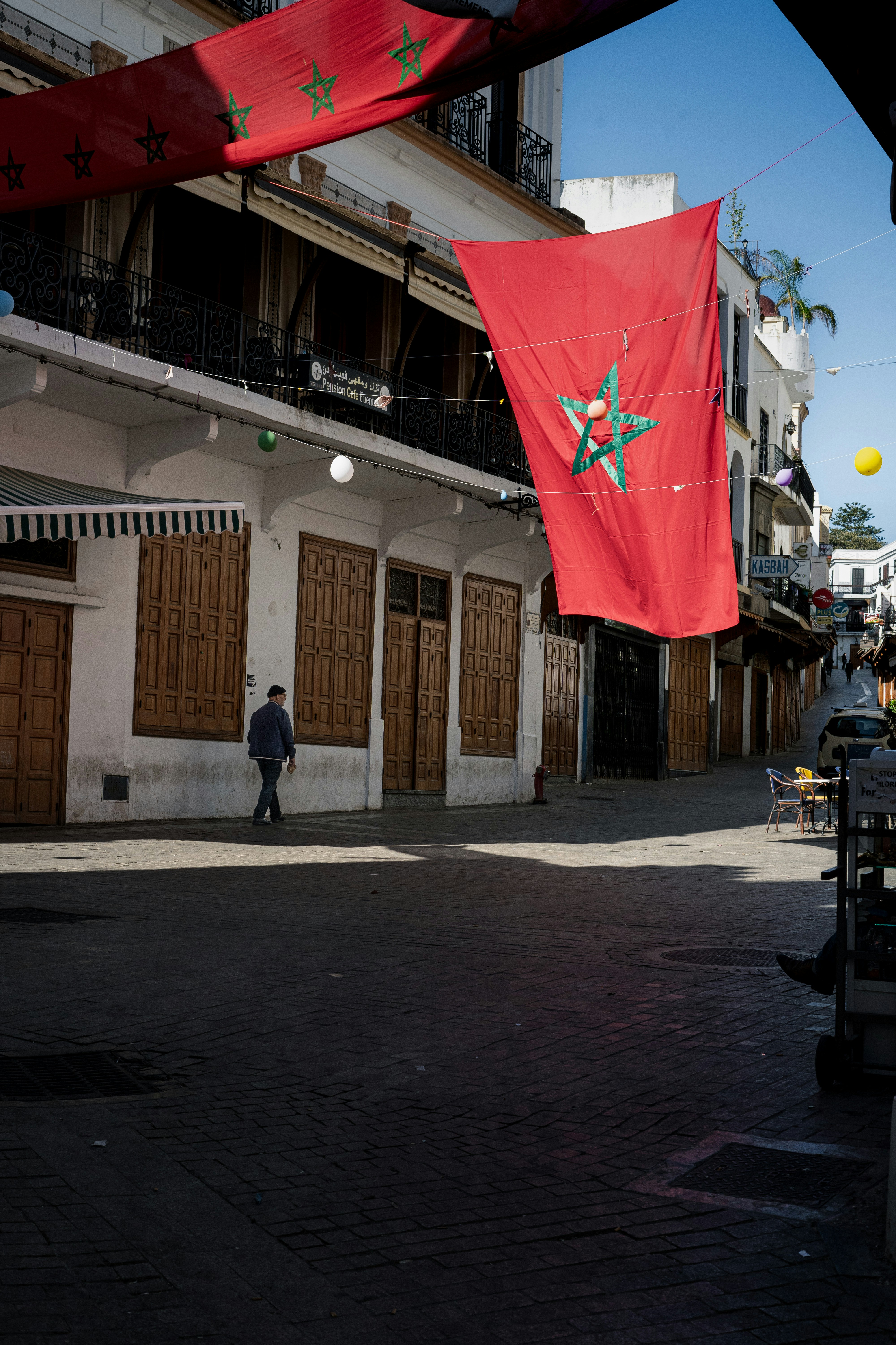Moroccan flag hangs over a street with buildings.