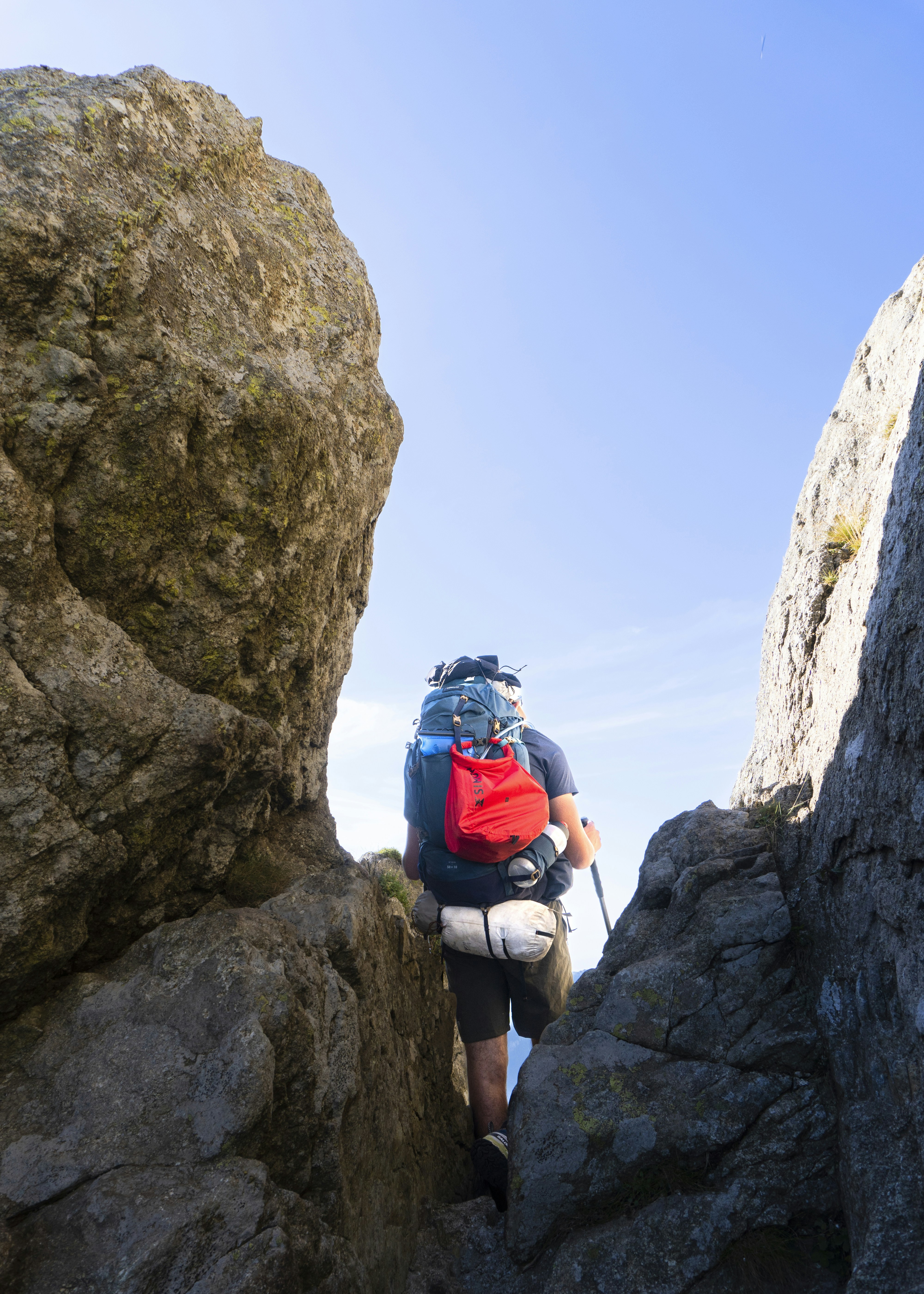 Hiker maneuvering through a narrow rocky passage on a bright day, showcasing the adventurous spirit of exploration.