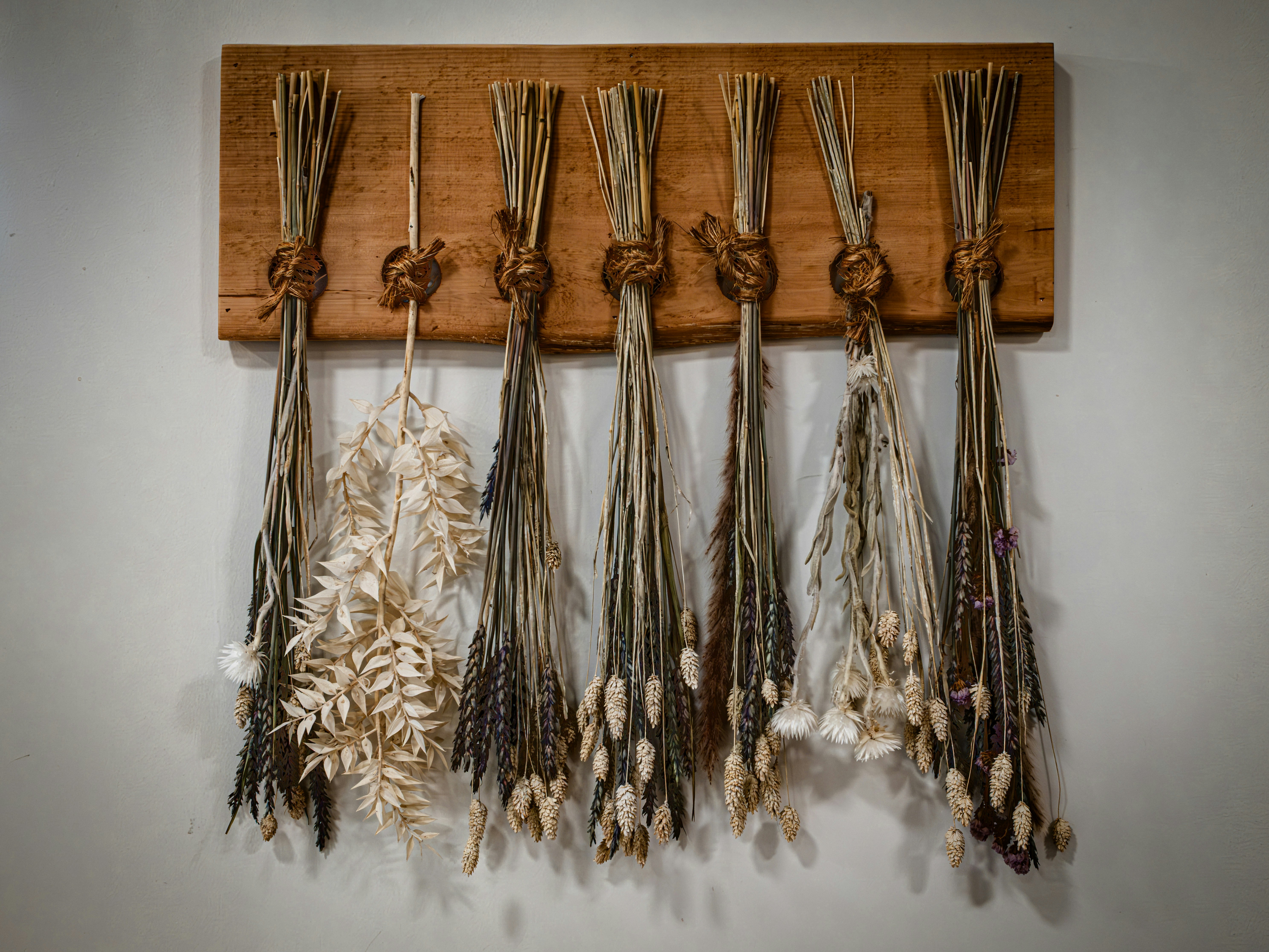Dried flowers hang on a wooden wall mount.