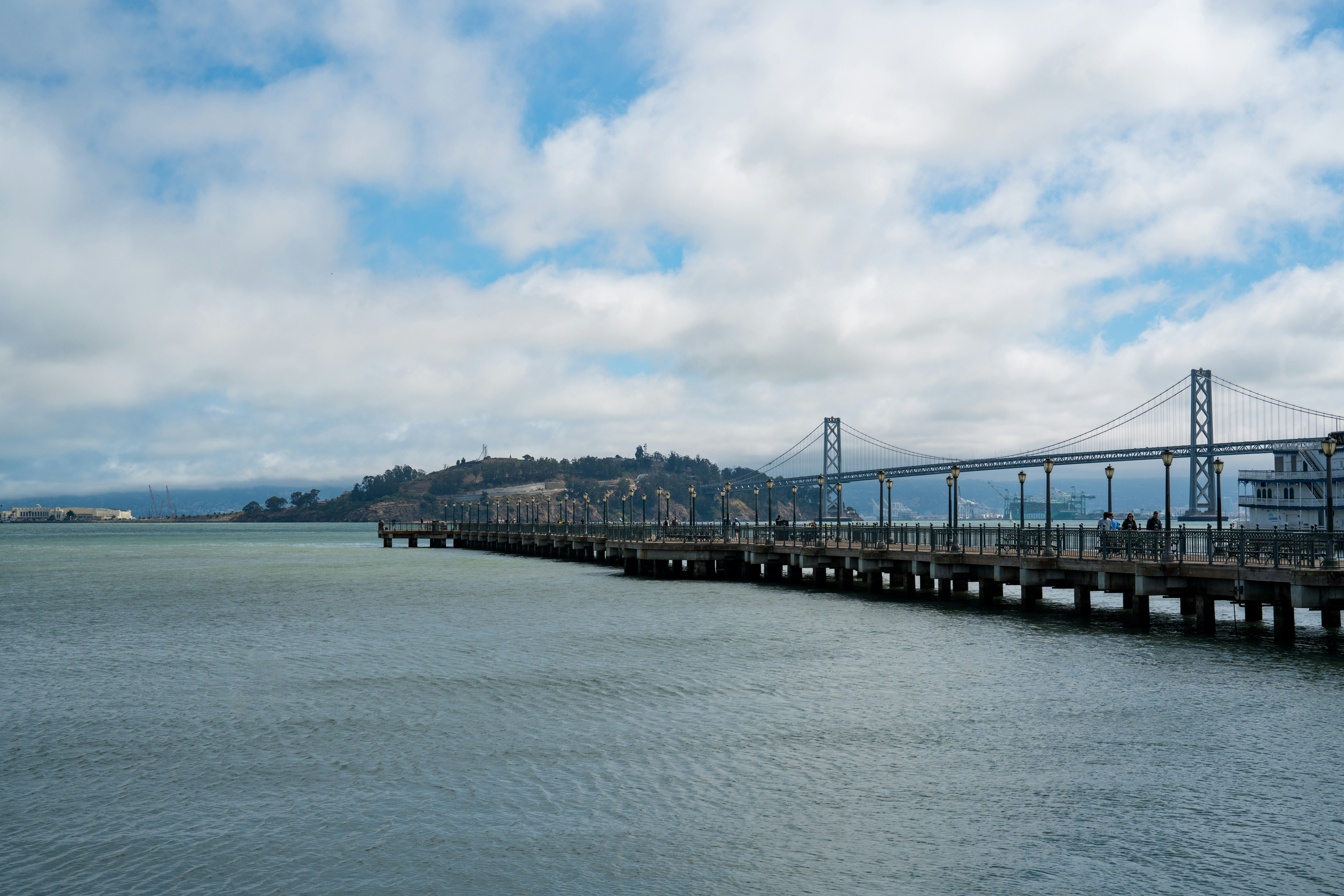 A long pier extends out over the water towards a bridge.