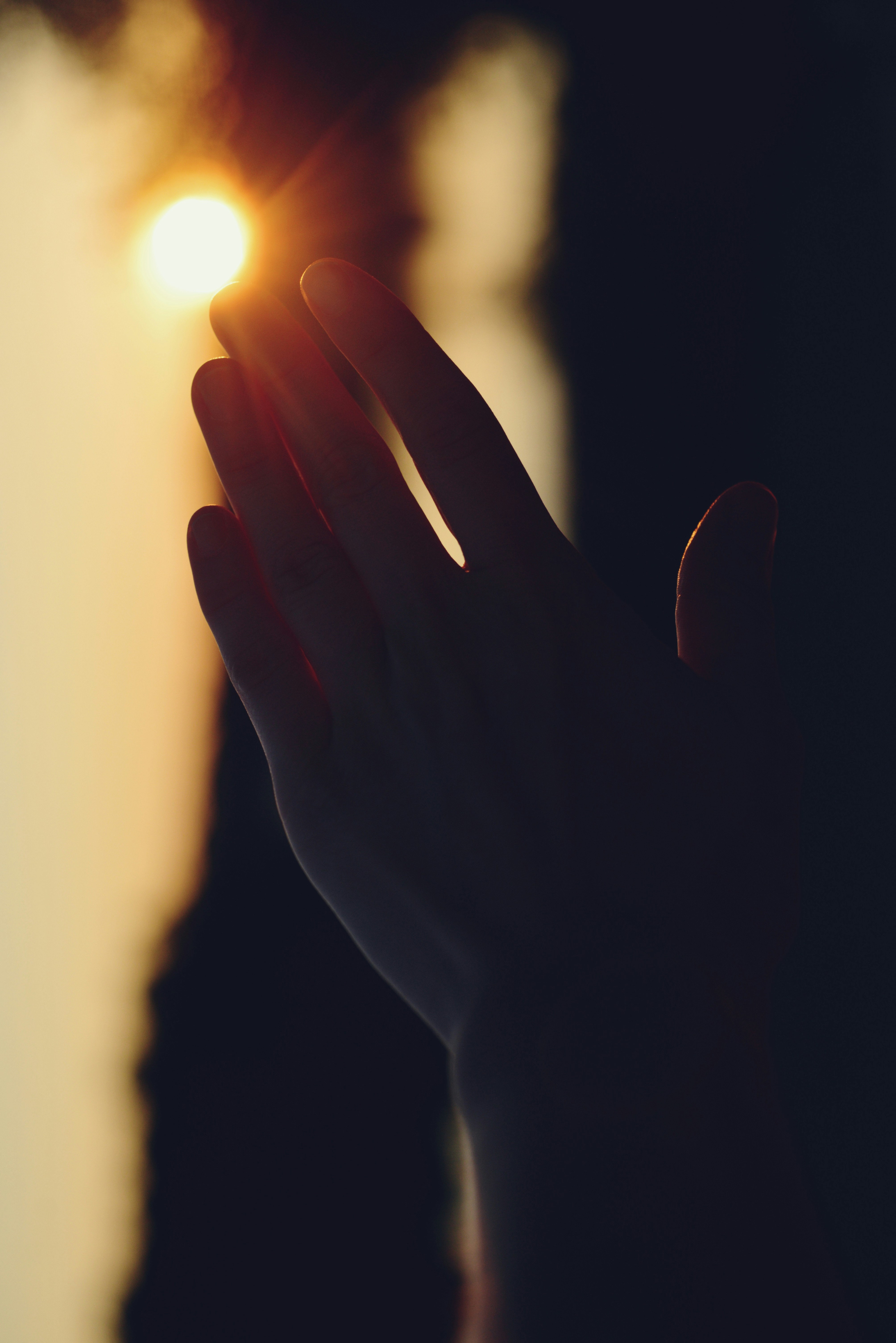Silhouette of a hand reaching towards the setting sun.