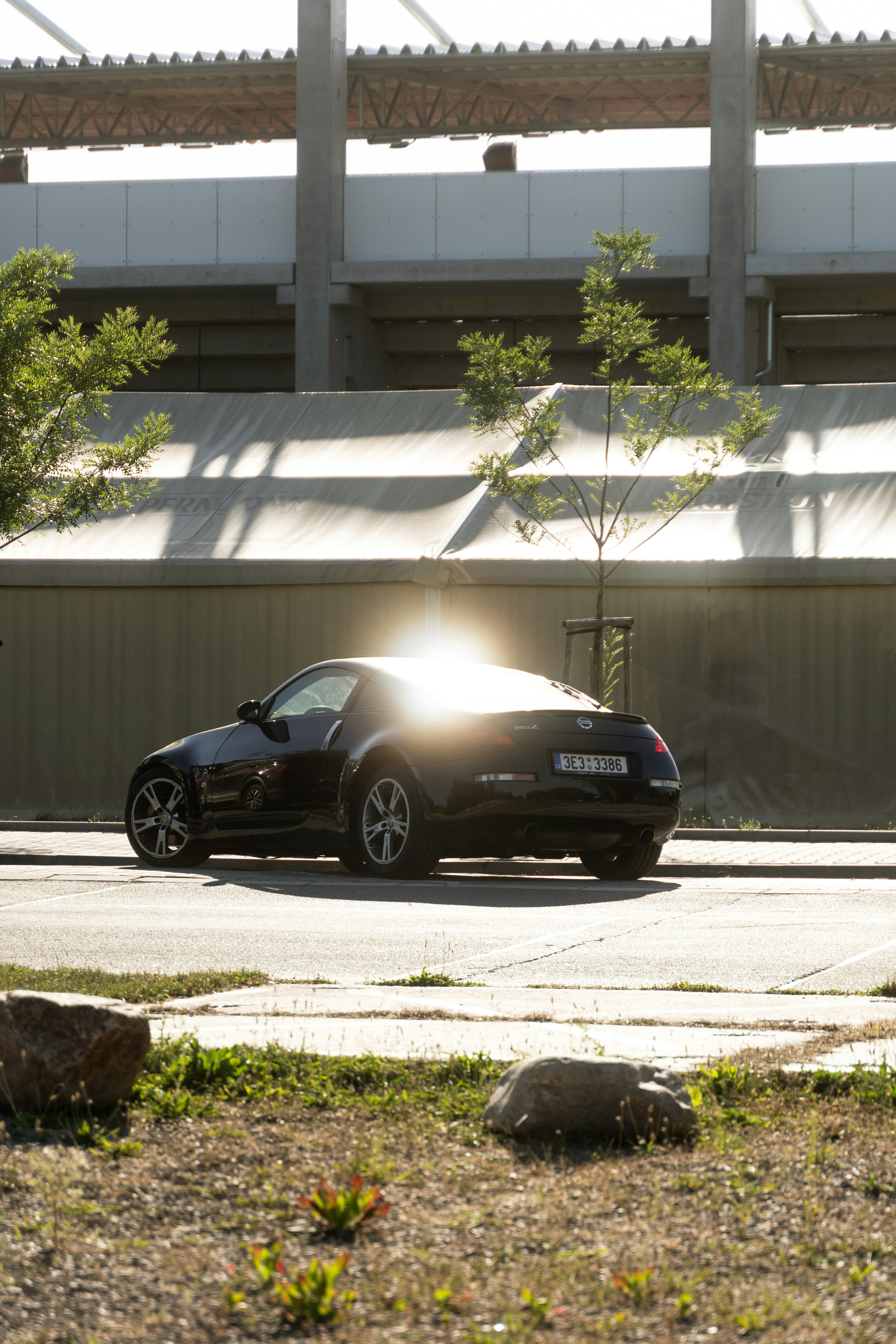 Sunlight is reflecting in the car’s window | Black sports car parked near stadium with sun flare