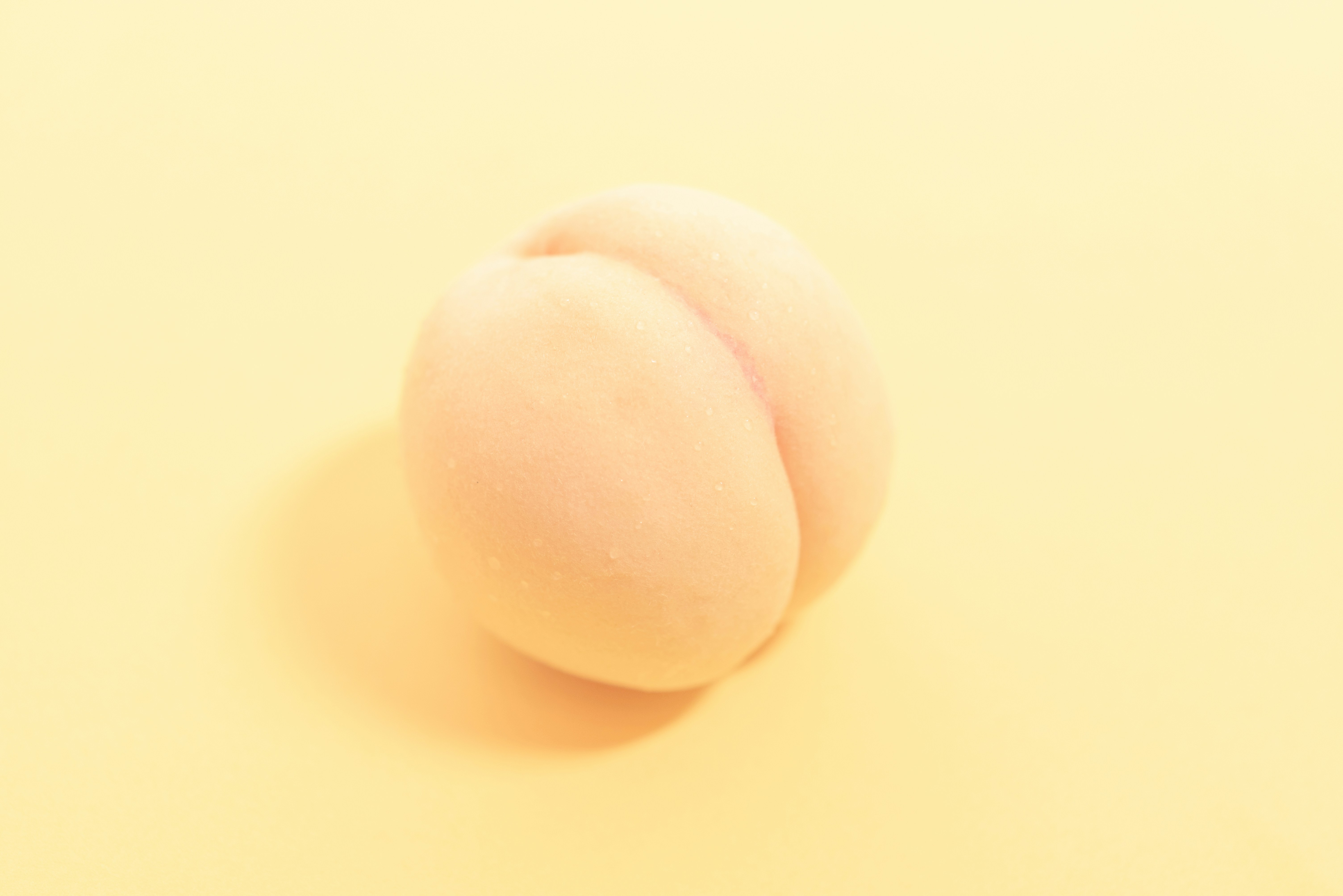 A perfectly ripe peach resting on a soft yellow background, showcasing its smooth texture and natural blush. The simplicity highlights the fruit's organic beauty.