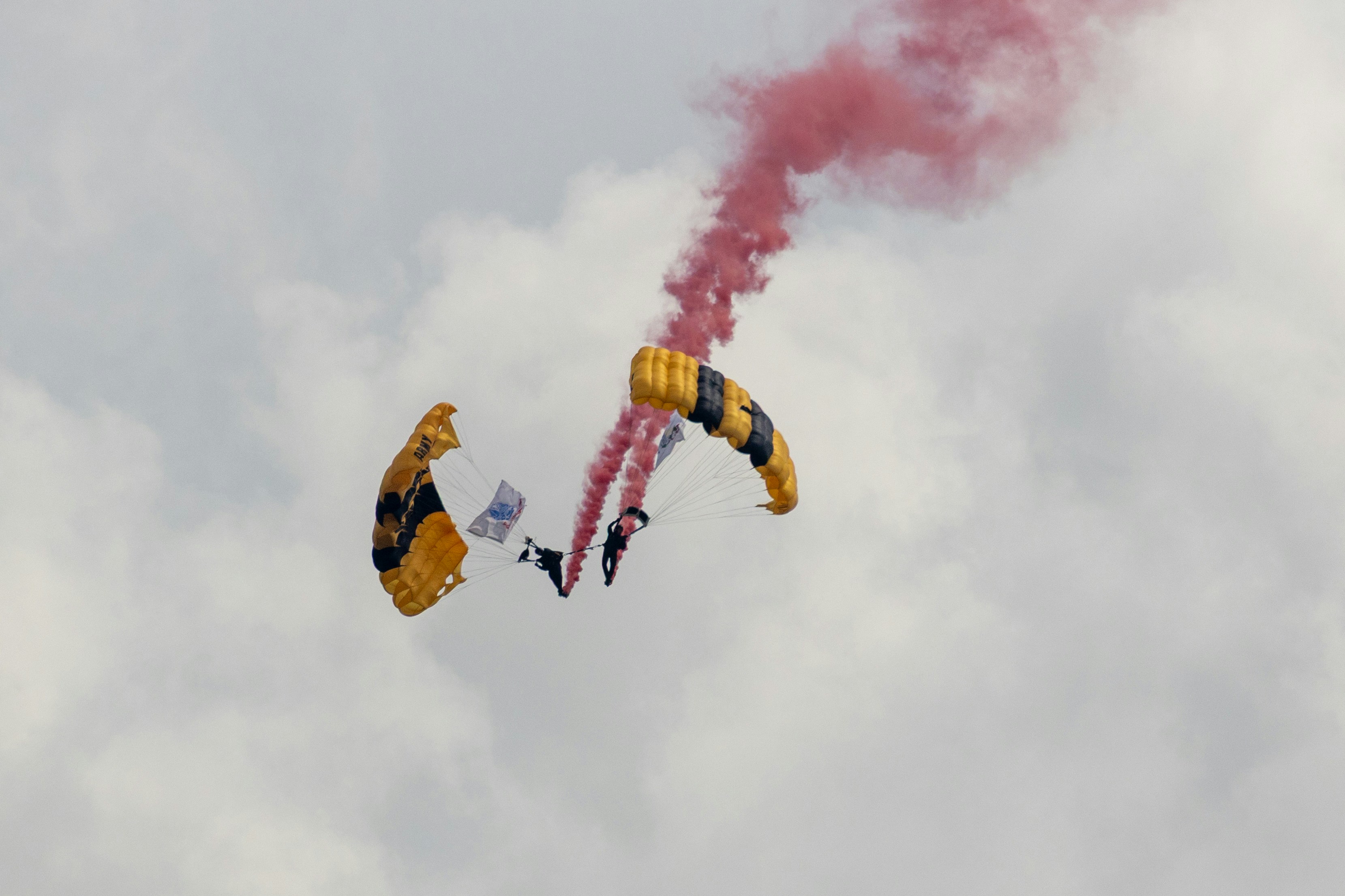 Two US Army Parachutists with smoke trailing behind them. | Skydivers with colorful parachutes and red smoke