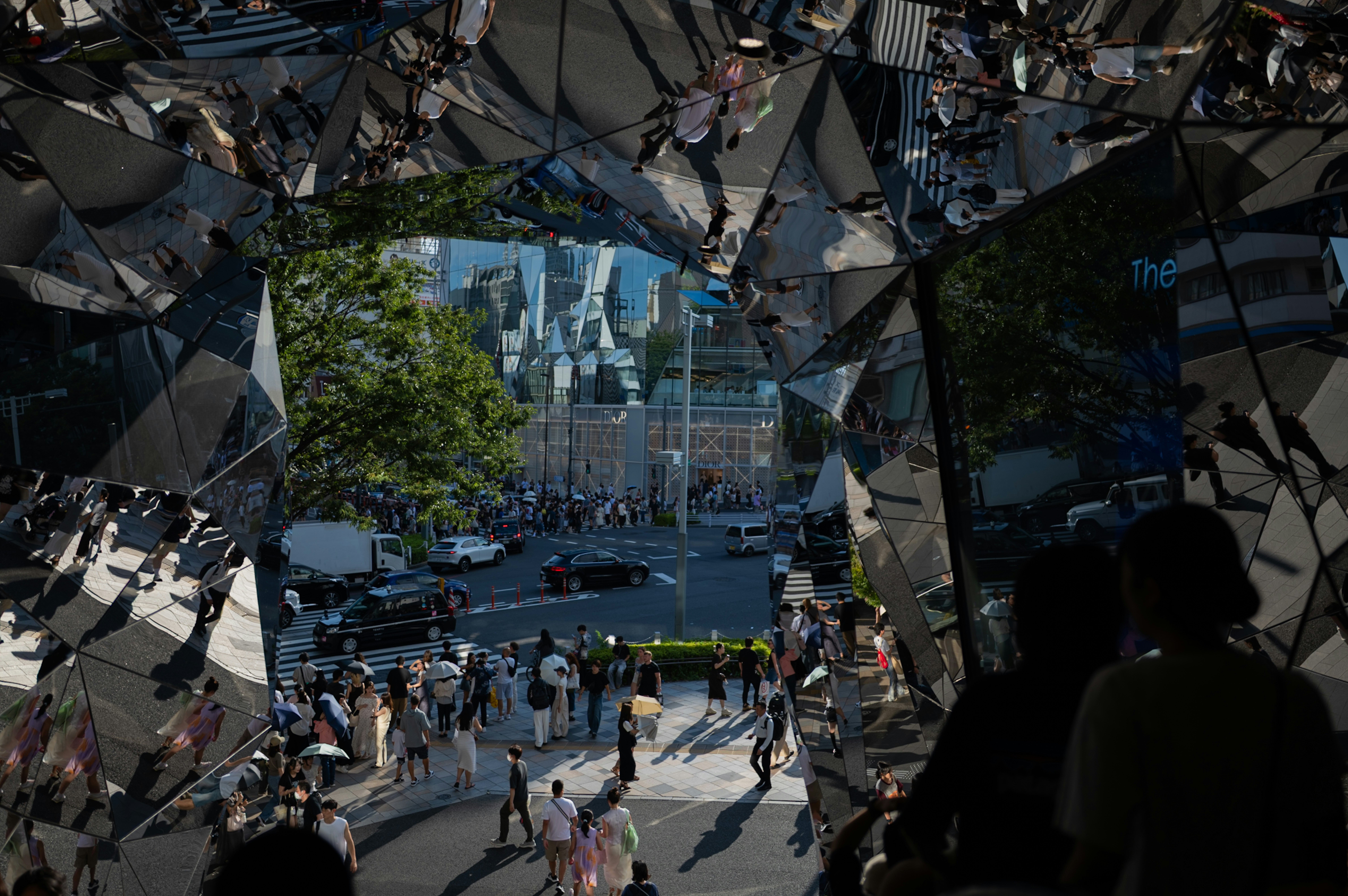 Crowd beneath a mirrored archway leading to a busy city square