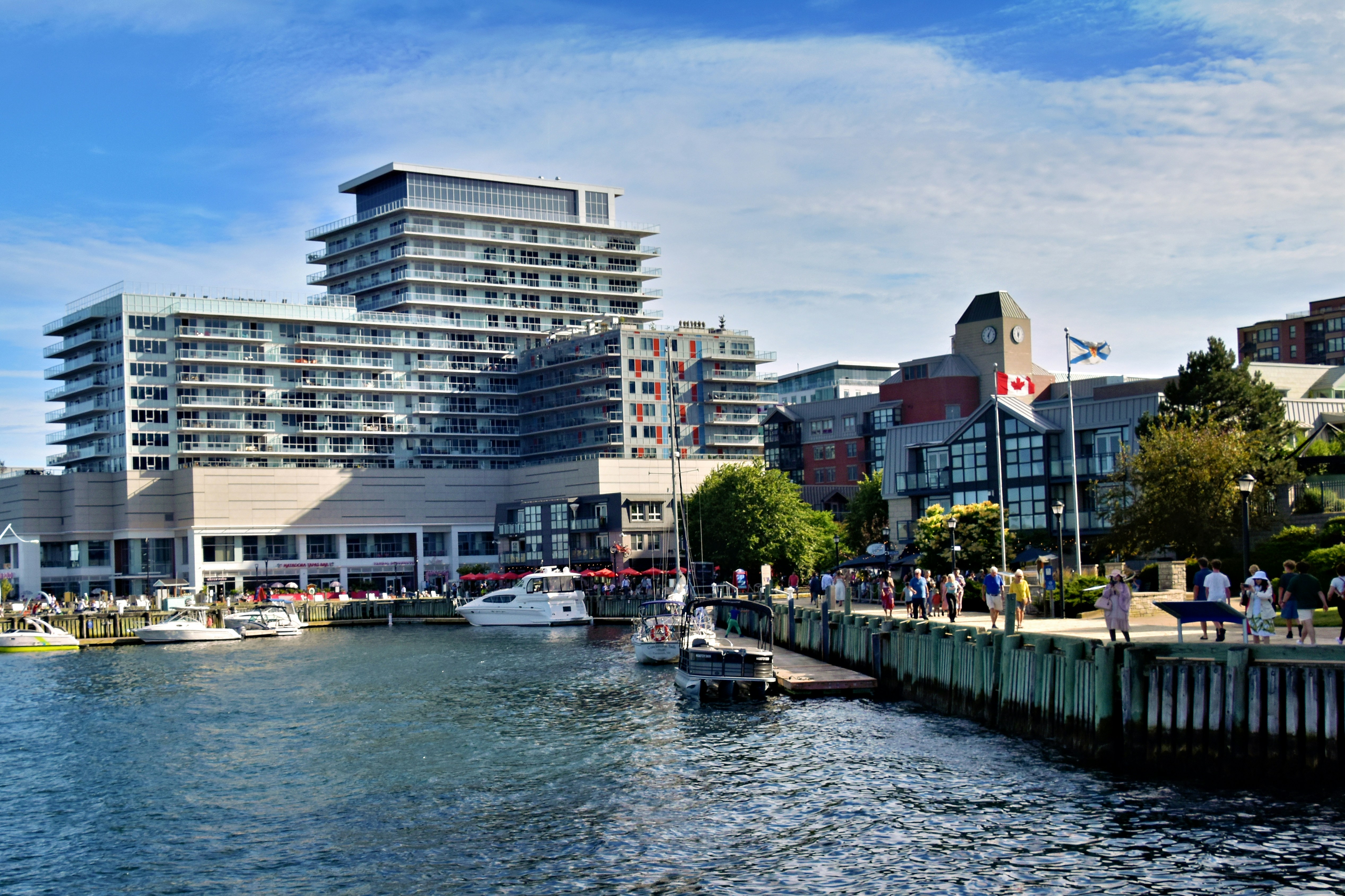 Modern buildings line a harbor with boats and people.