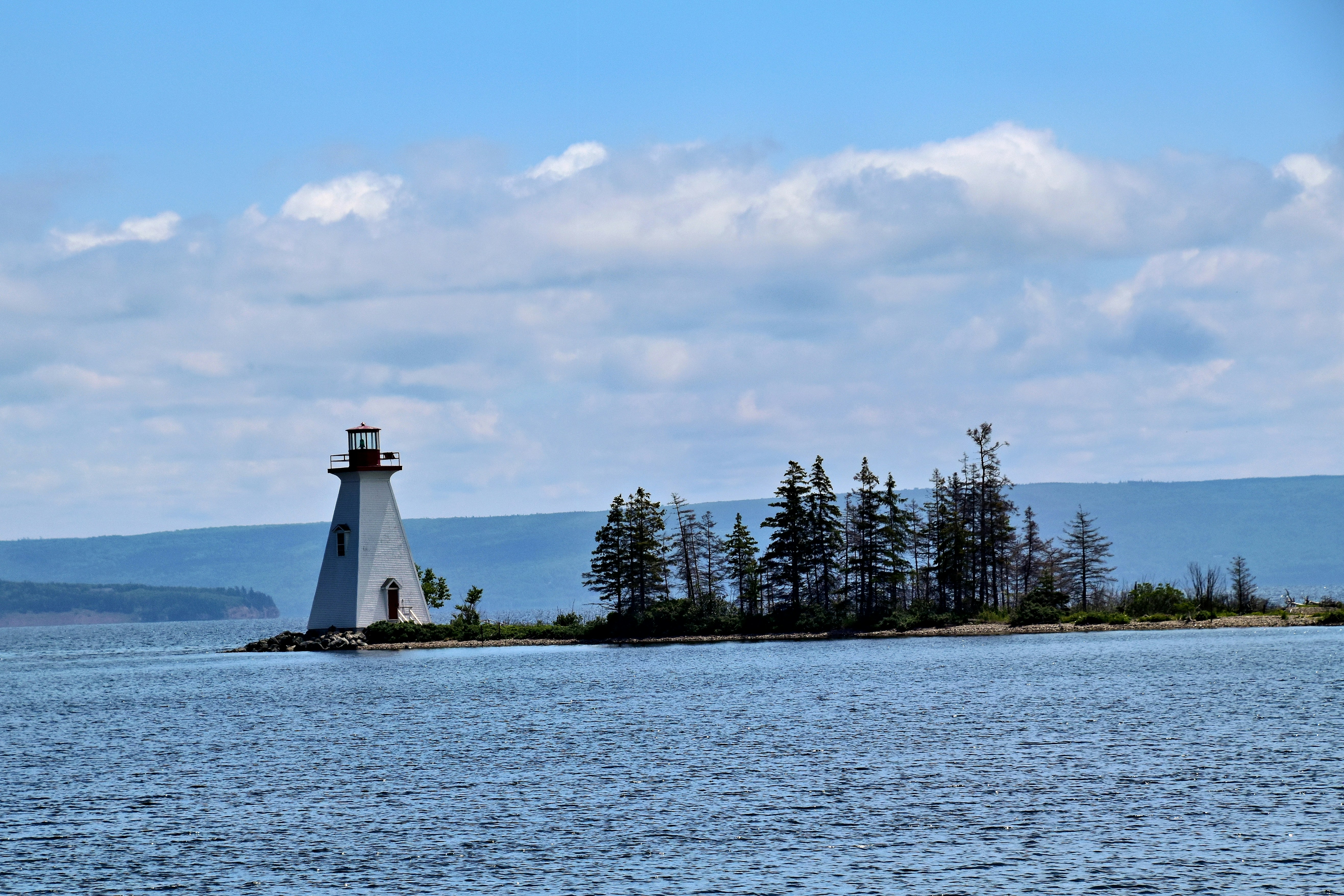 Lighthouse on a small island with trees under blue sky