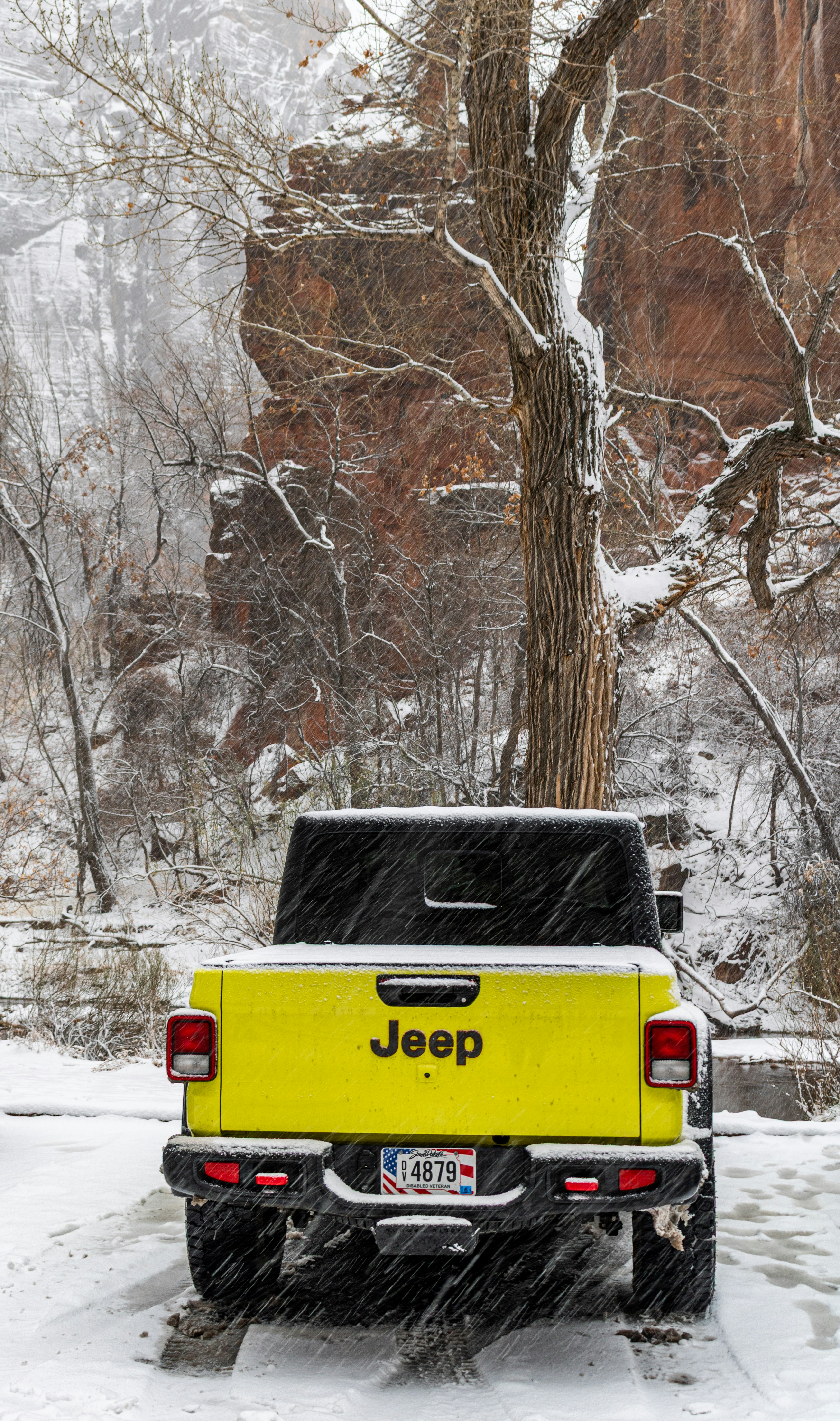 A Jeep Gladiator is parked in the snow at Zion National Park | Yellow jeep truck parked in snowy landscape