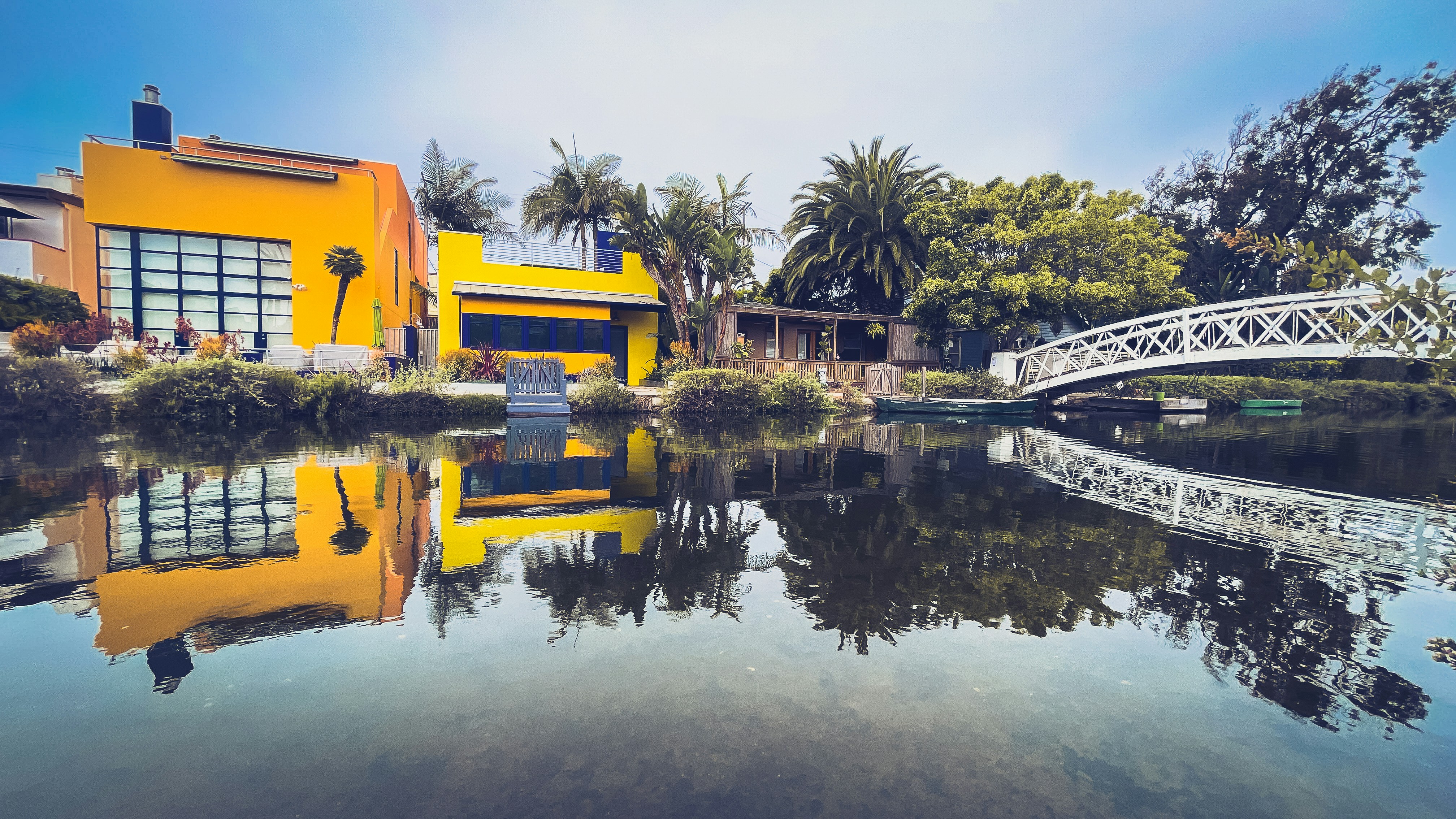 Colorful modern architecture beside a serene waterway, with a white bridge reflecting in the calm water.