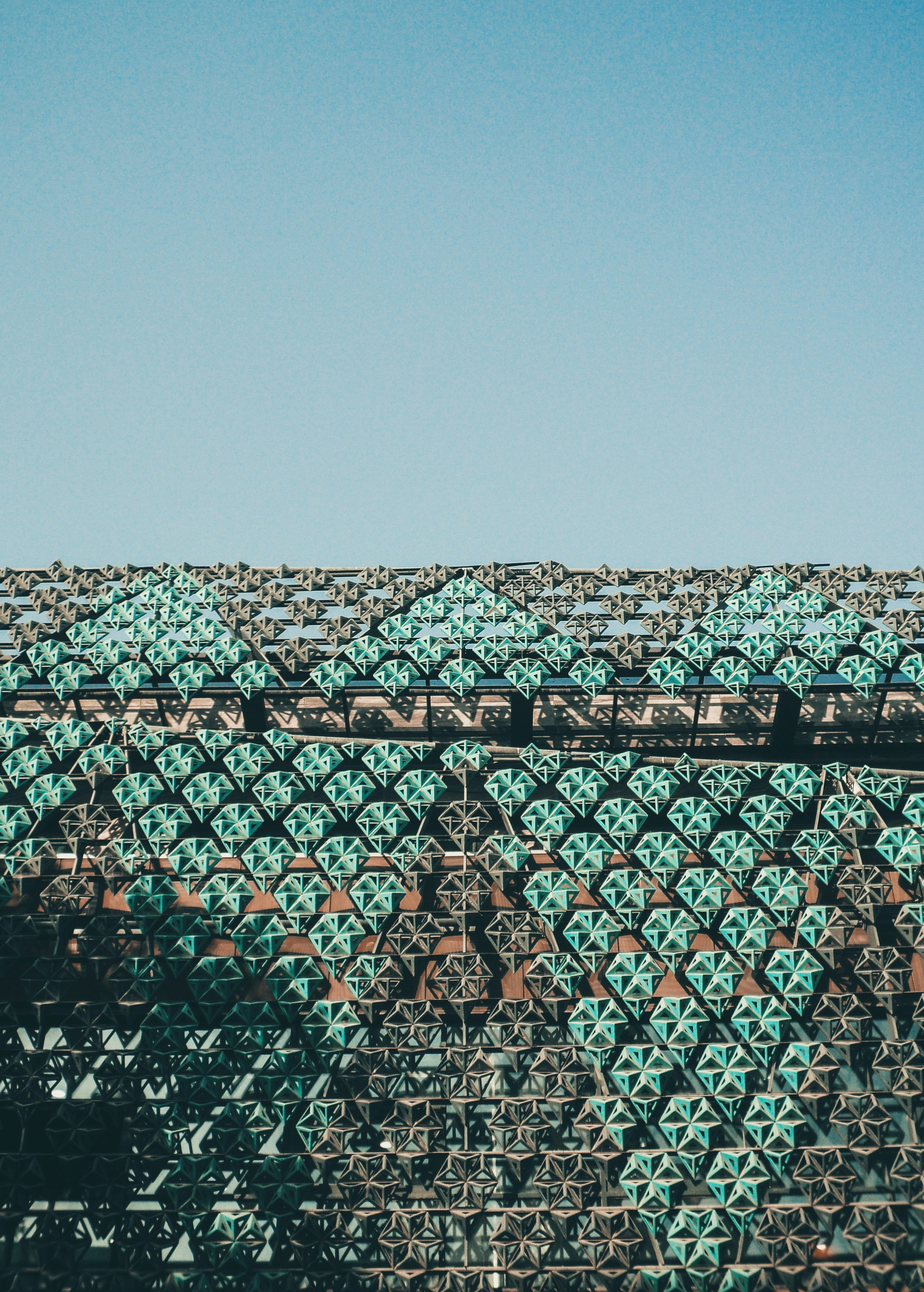 A thousand diamonds on a single canvas. | Geometric pattern of green and gray structures against blue sky