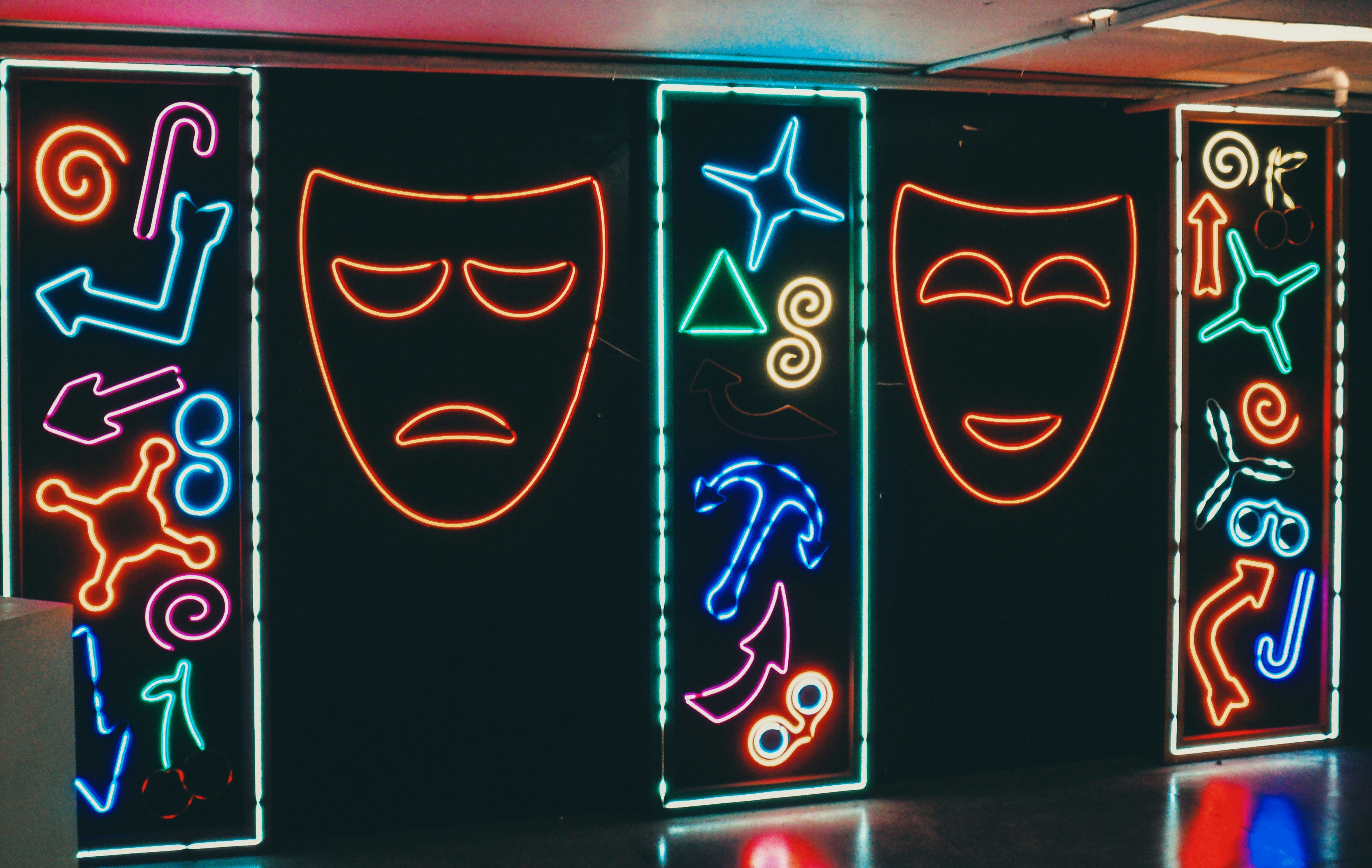 Where a city's soul is lit by neon. | Neon signs depict happy and sad theater masks.
