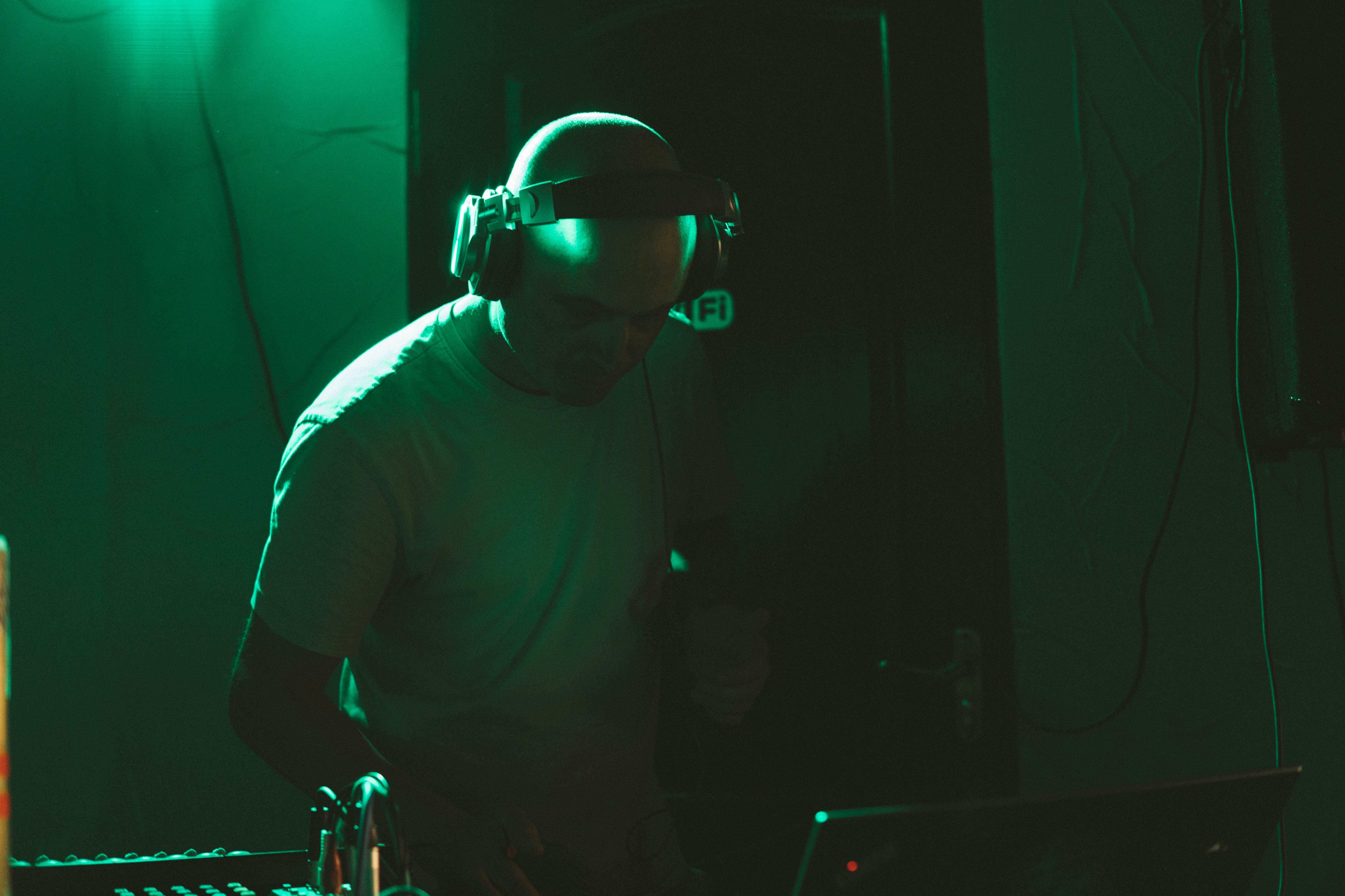 Dj wearing headphones plays music in a green lit room