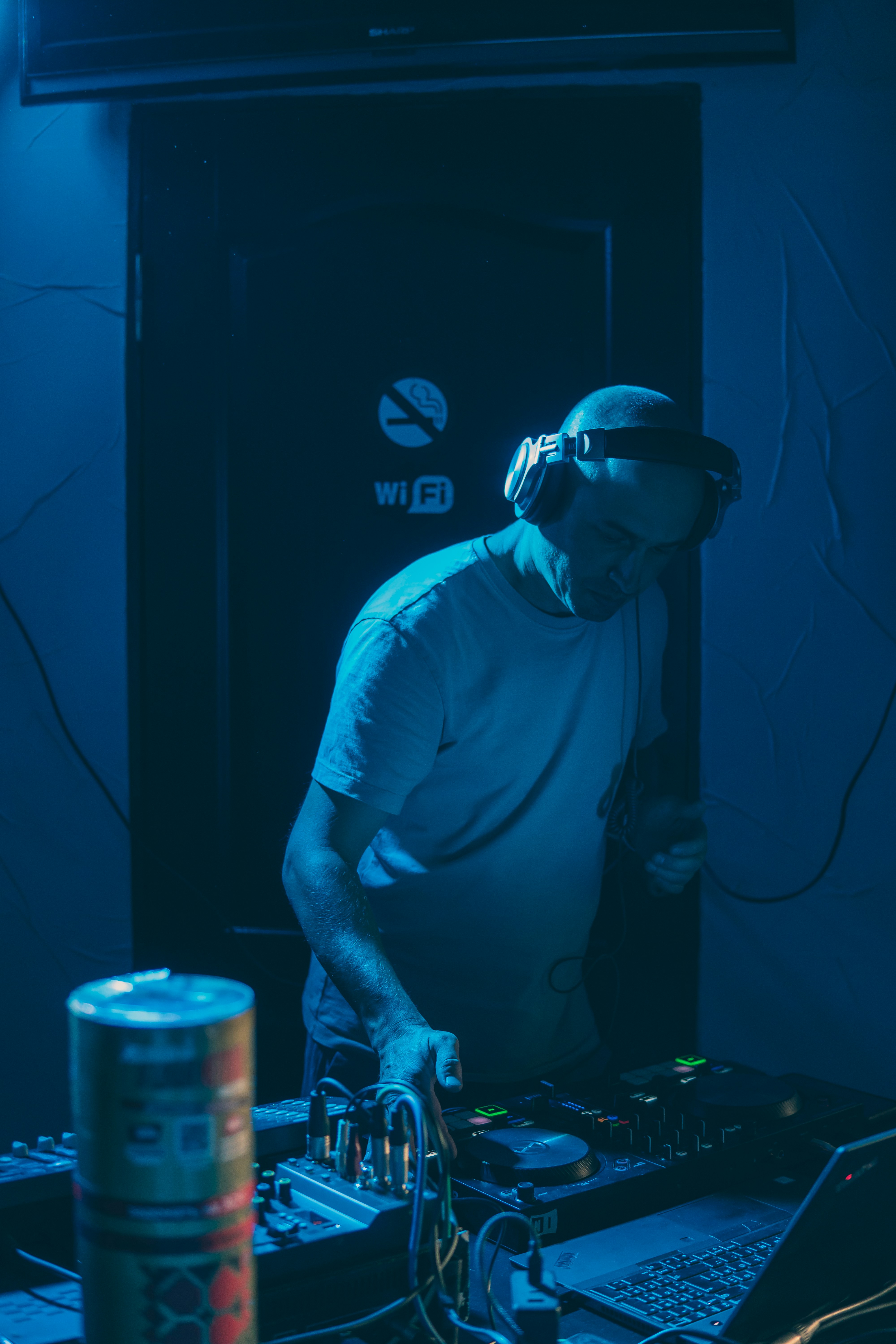 DJ immersed in mixing tracks, surrounded by vibrant blue lighting and music equipment. A canister sits prominently on the table.