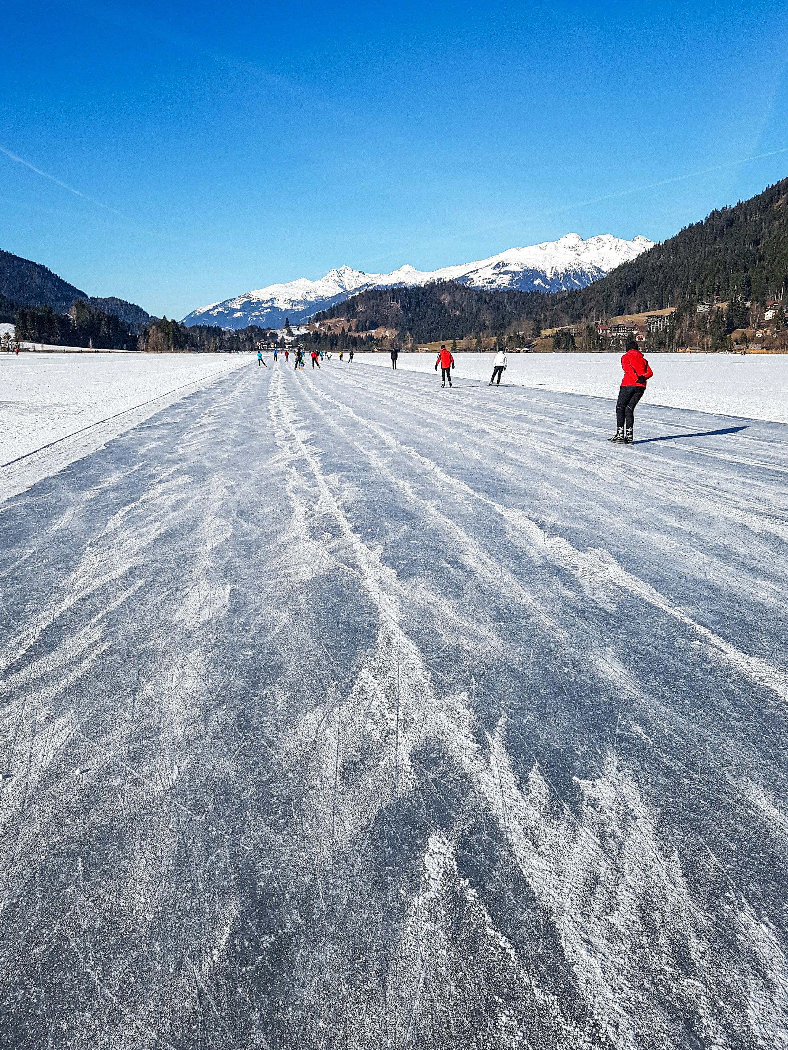 people doing ice-skating on a frozen lake in winter | People ice skating on a frozen lake with mountains