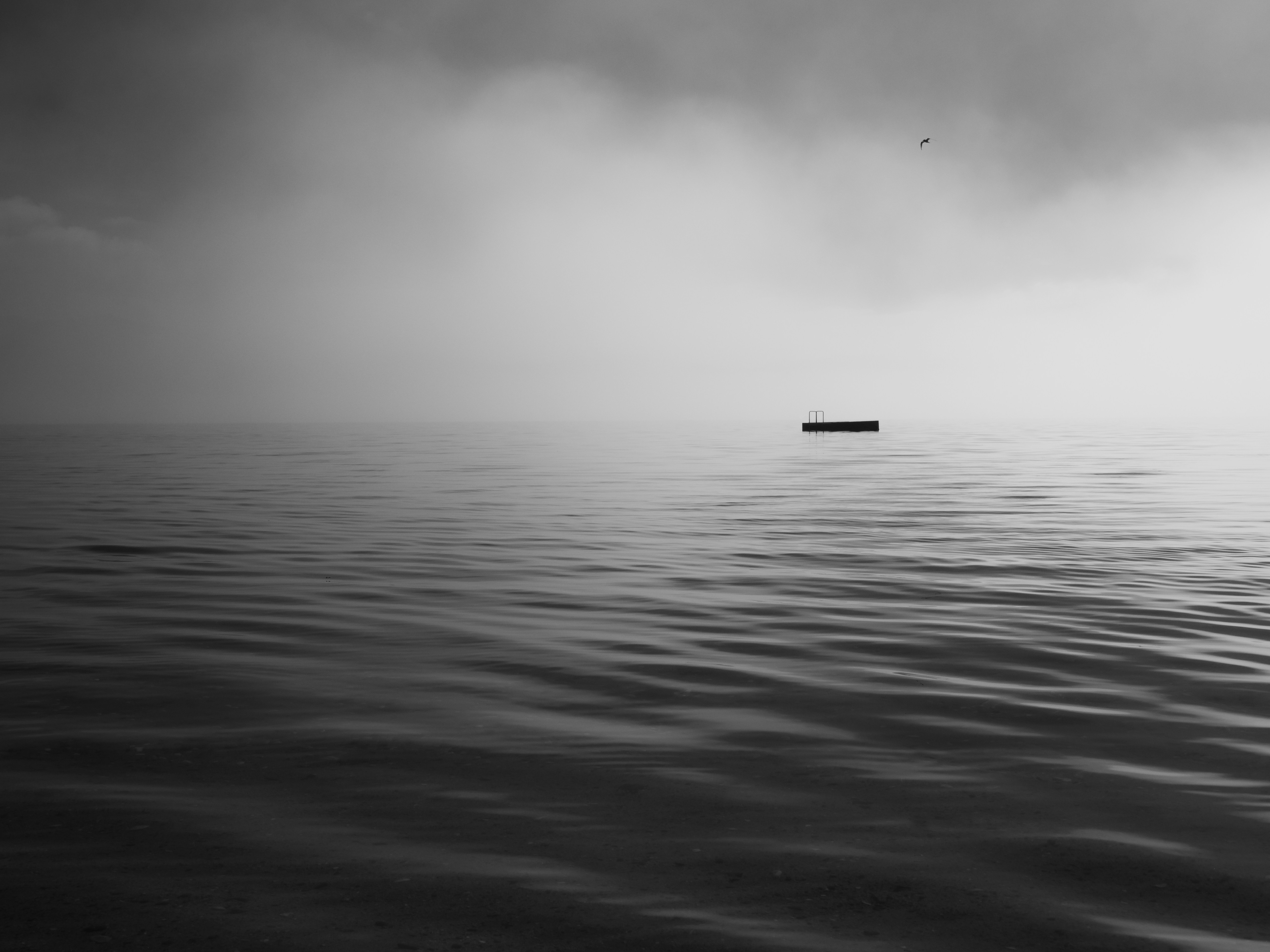 a single swimming platform in an foggy ocean | A lone boat drifts on a misty, calm sea.