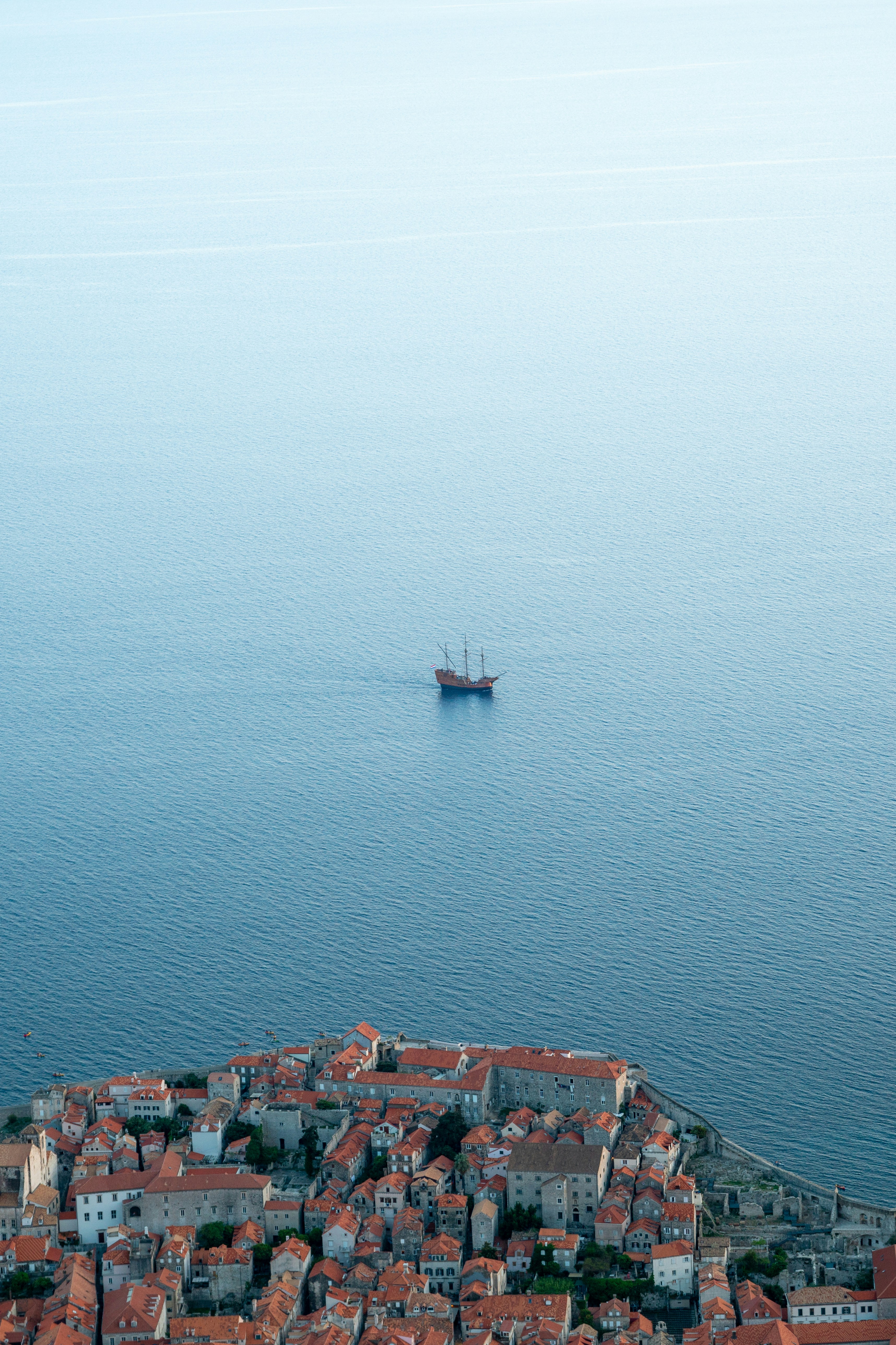 Old ship on the coast of Dubrovnik | A red ship sails on a calm blue ocean near a coastal city.
