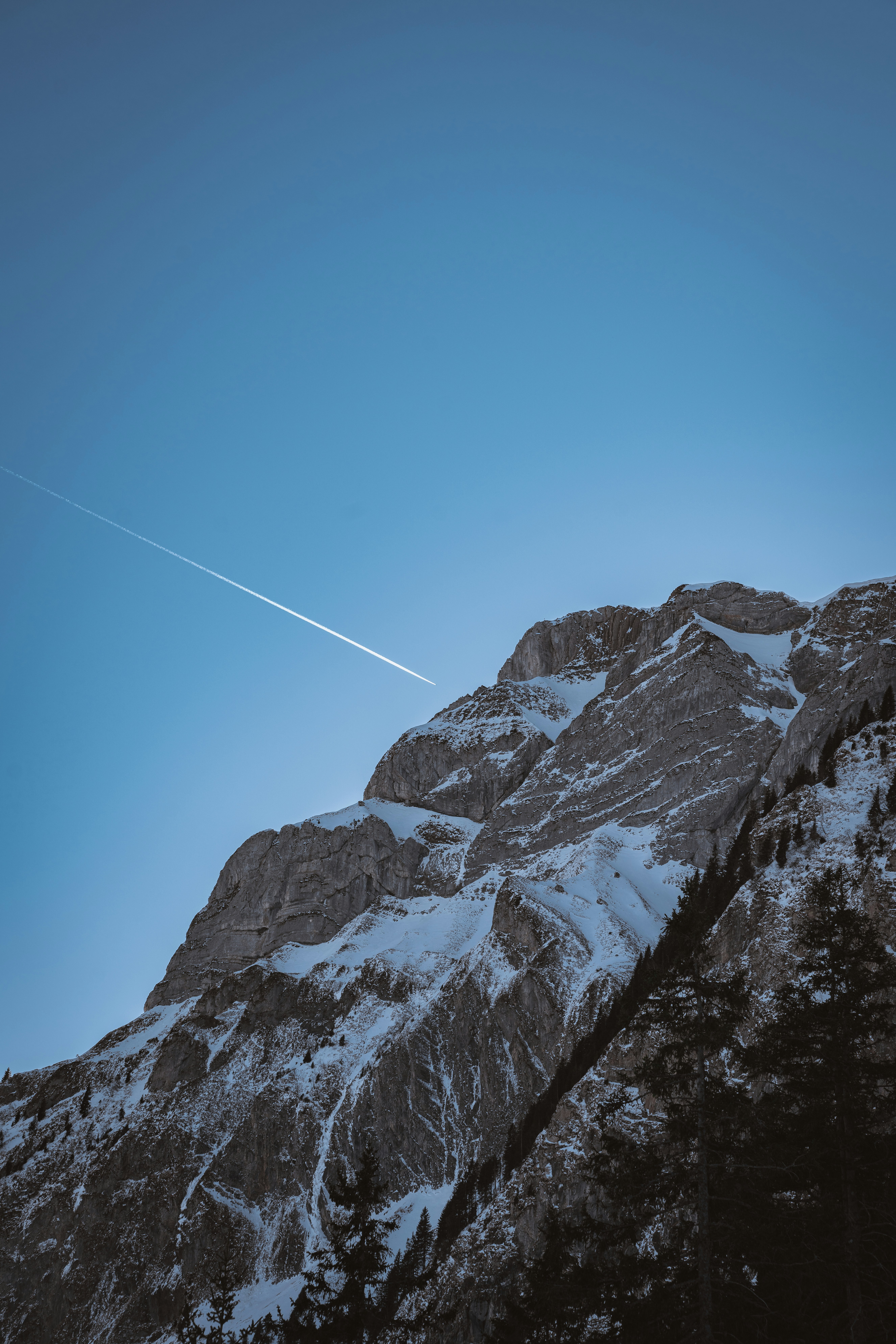 Snow-covered mountain peak under a clear blue sky, with a jet stream cutting across the horizon.