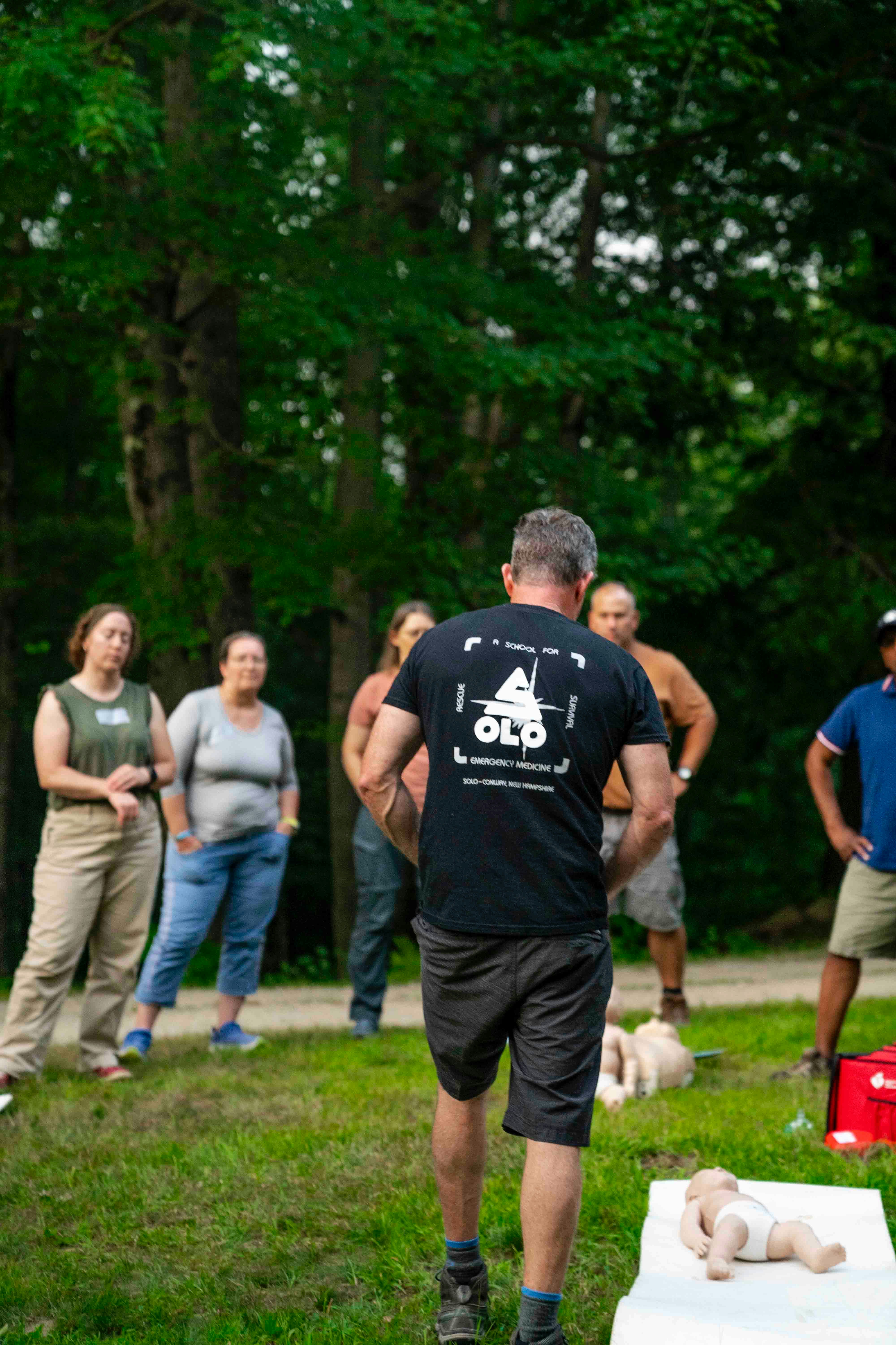 Group of individuals engaged in a hands-on training session, focusing on emergency response techniques with practice dummies on the ground.