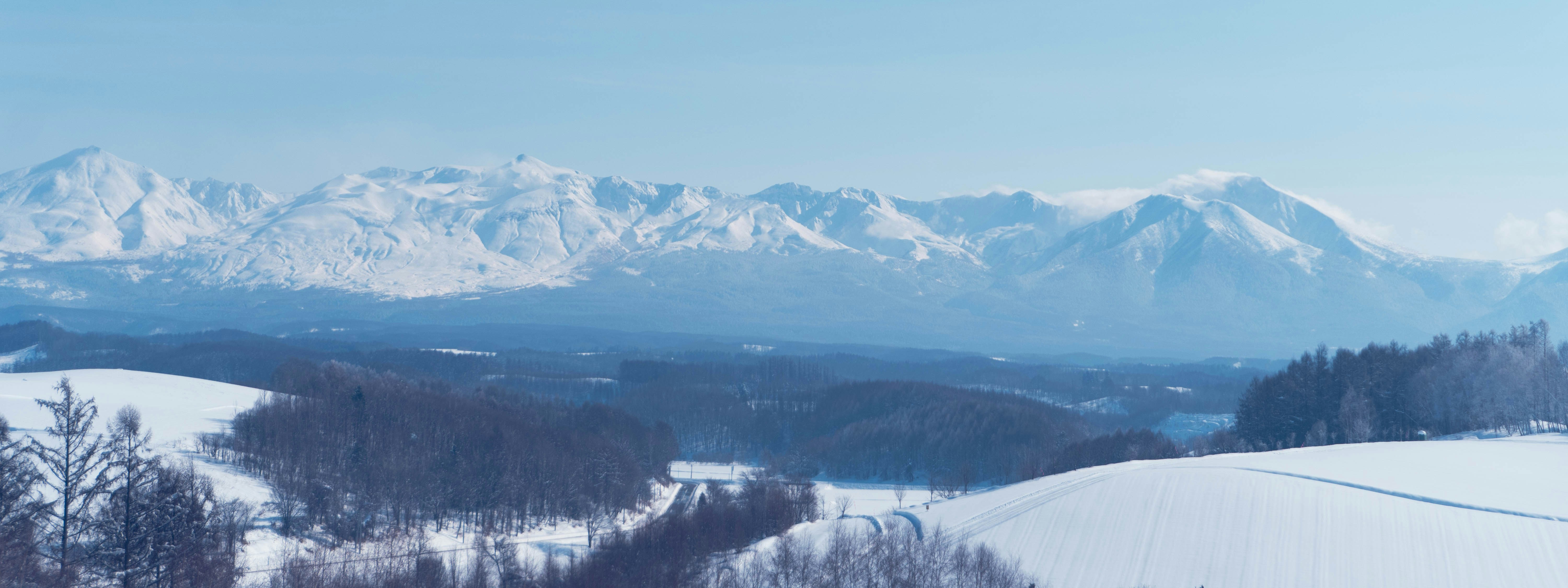 Snow-covered mountains rise majestically against a clear blue sky, with rolling hills blanketed in white below.
