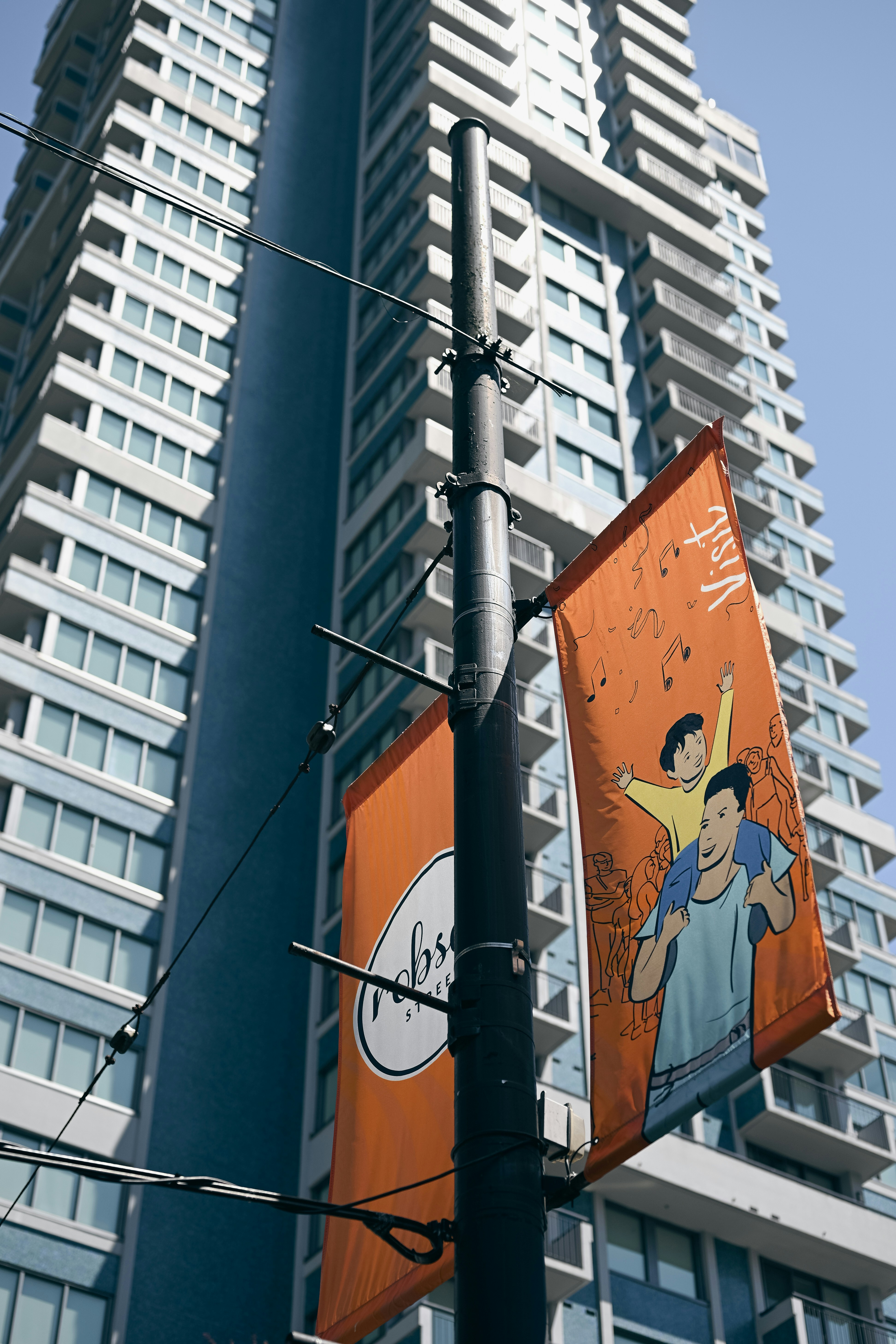 Orange banners hang from a pole with a building behind.